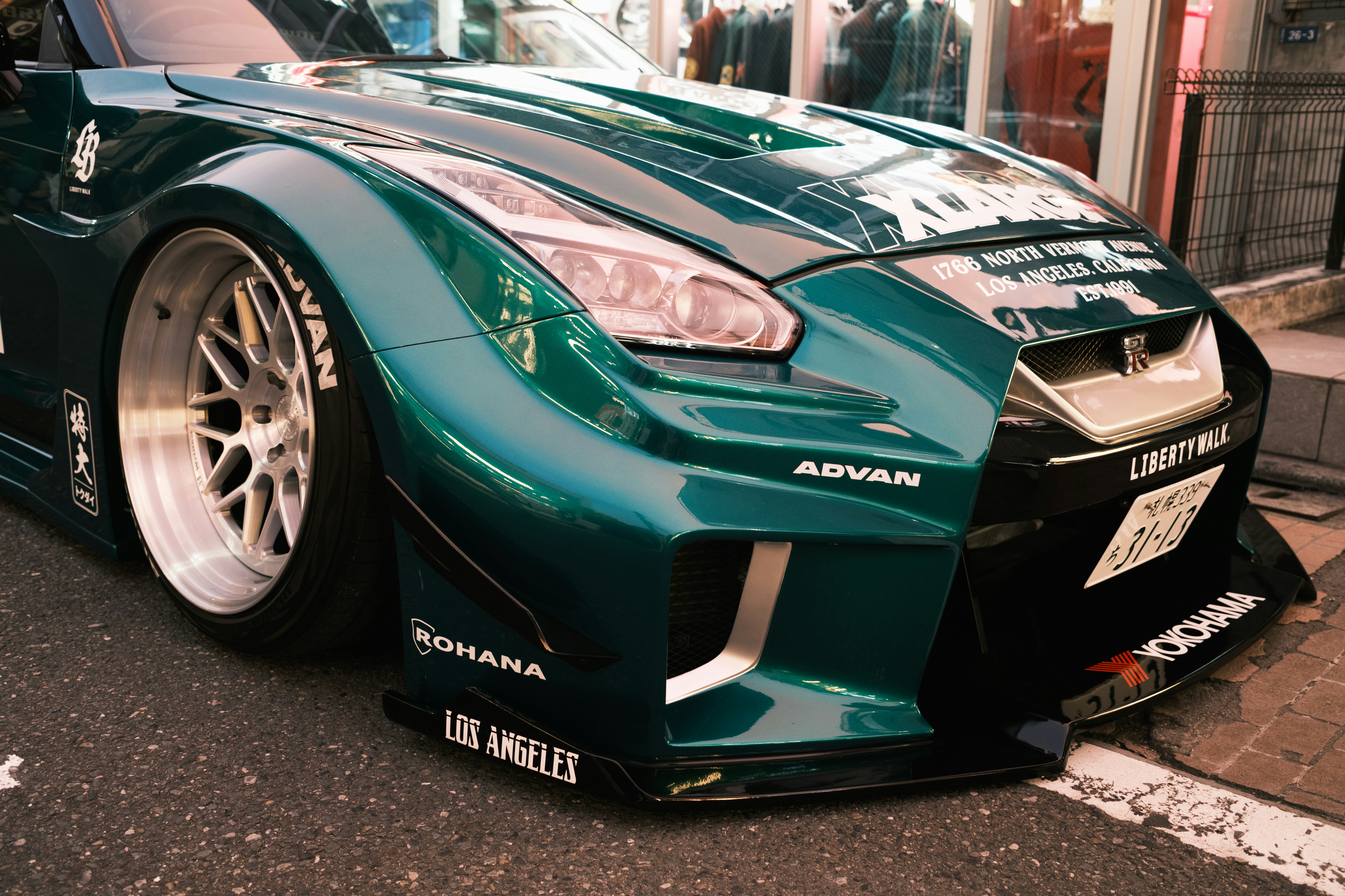 Teal Nissan-leaning stance: low front bumper and wheel showcase in urban night chrome