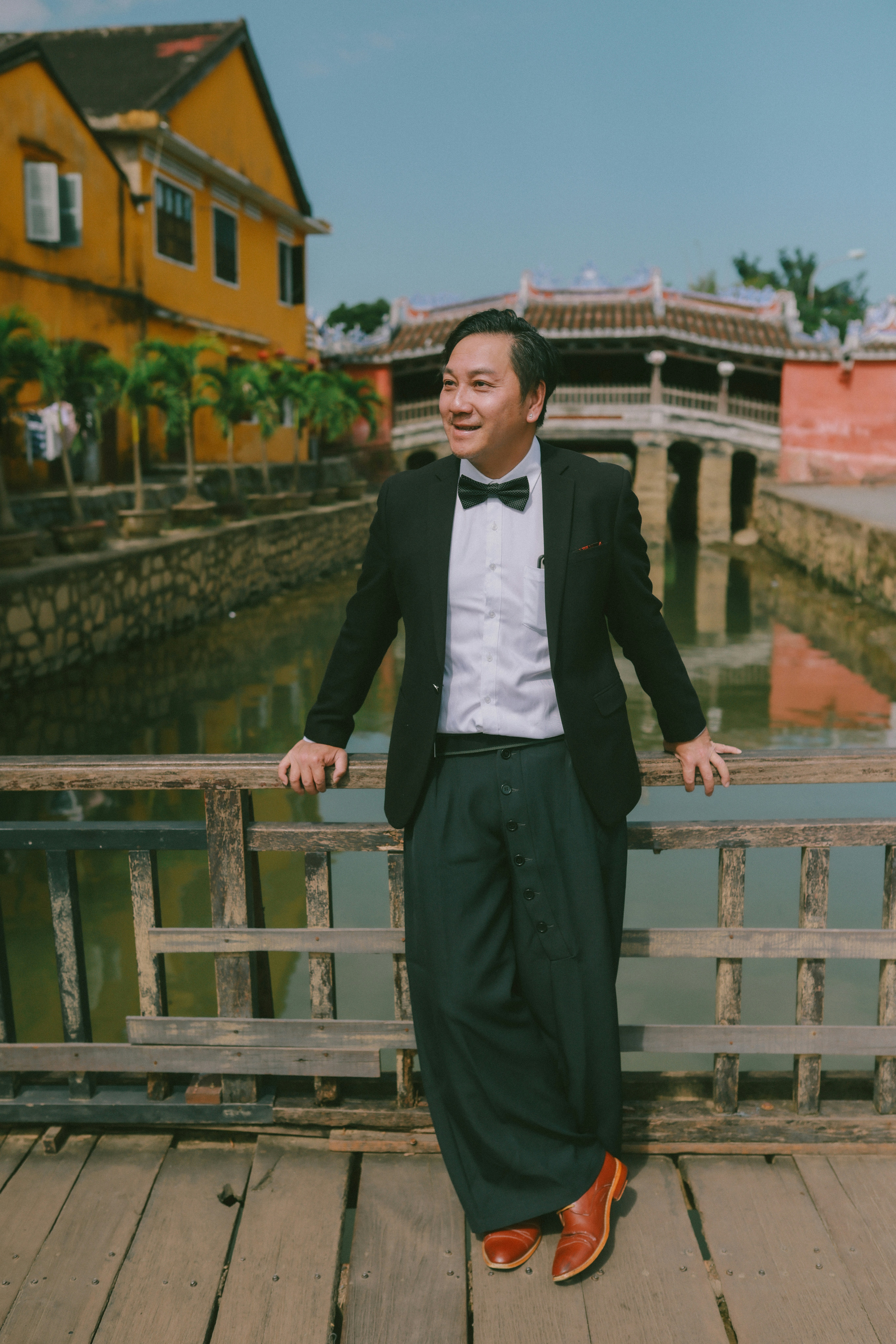 Gentleman in Black Bow Tie Stands by a Riverfront Bridge