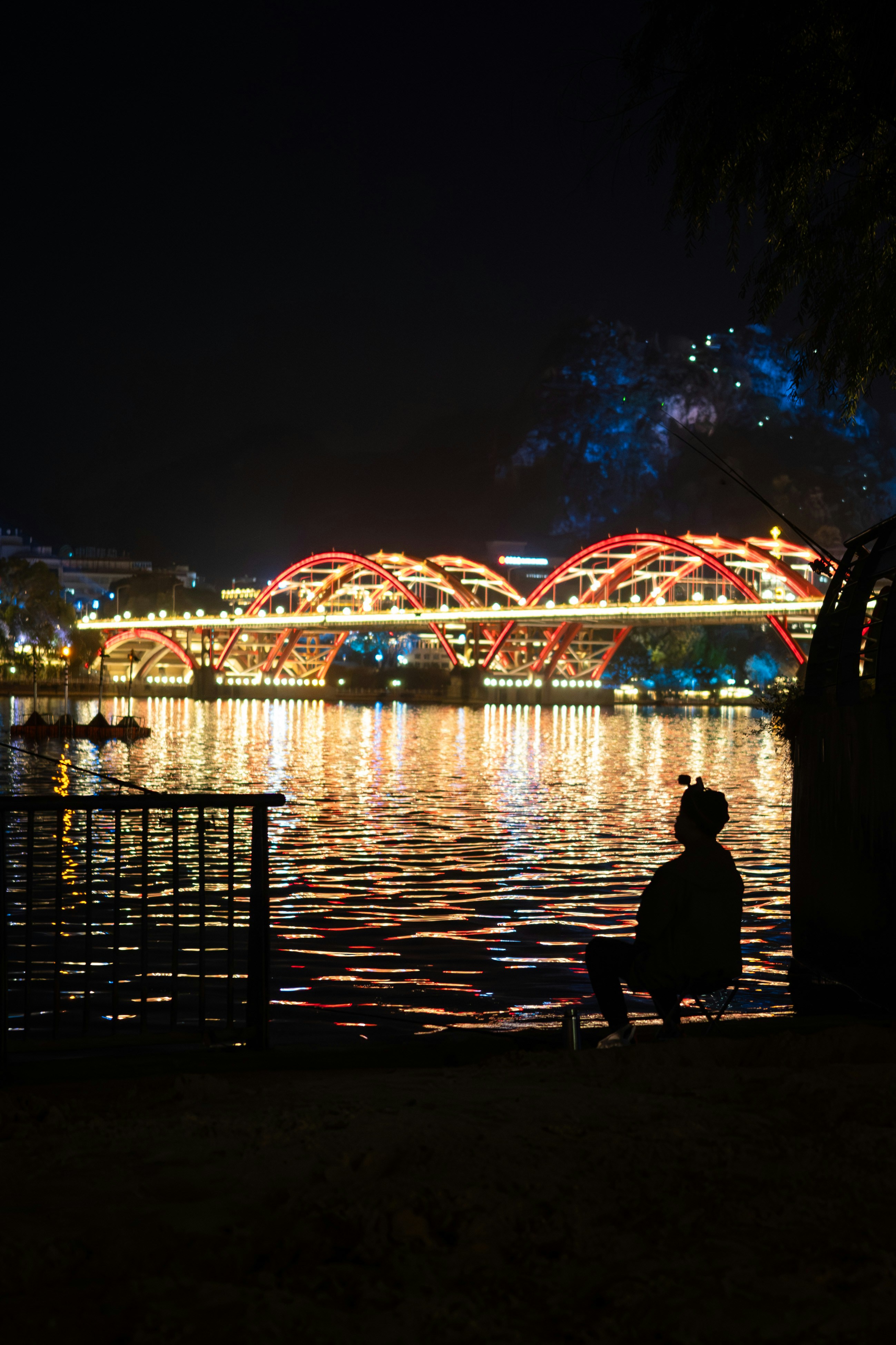 Nighttime Riverside Blues: A Lone Fisherman Beneath Neon Arches