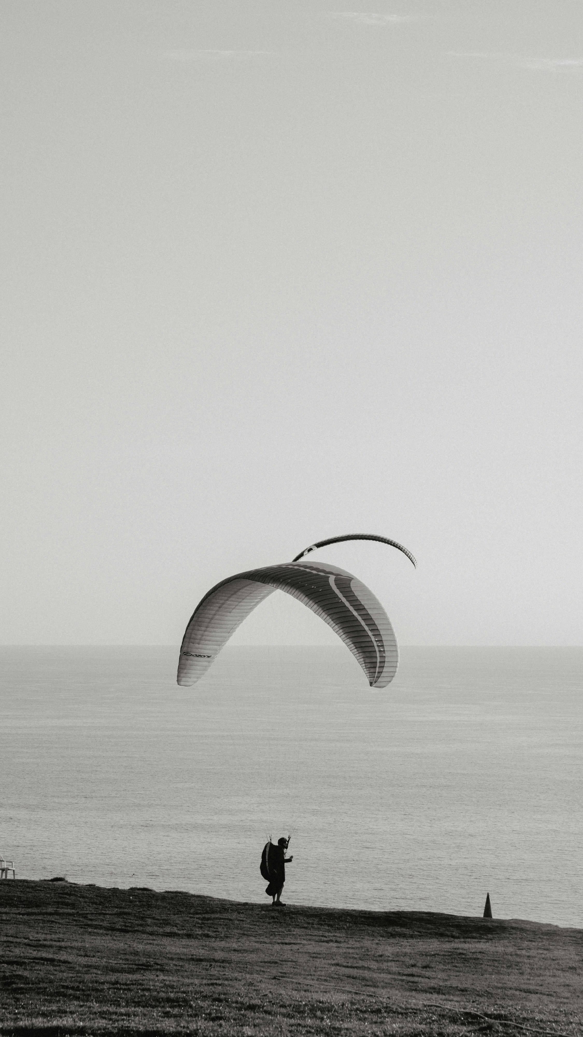 Glide Above the Cliff: A Solo Paraglider Emerges Over Quiet Seas
