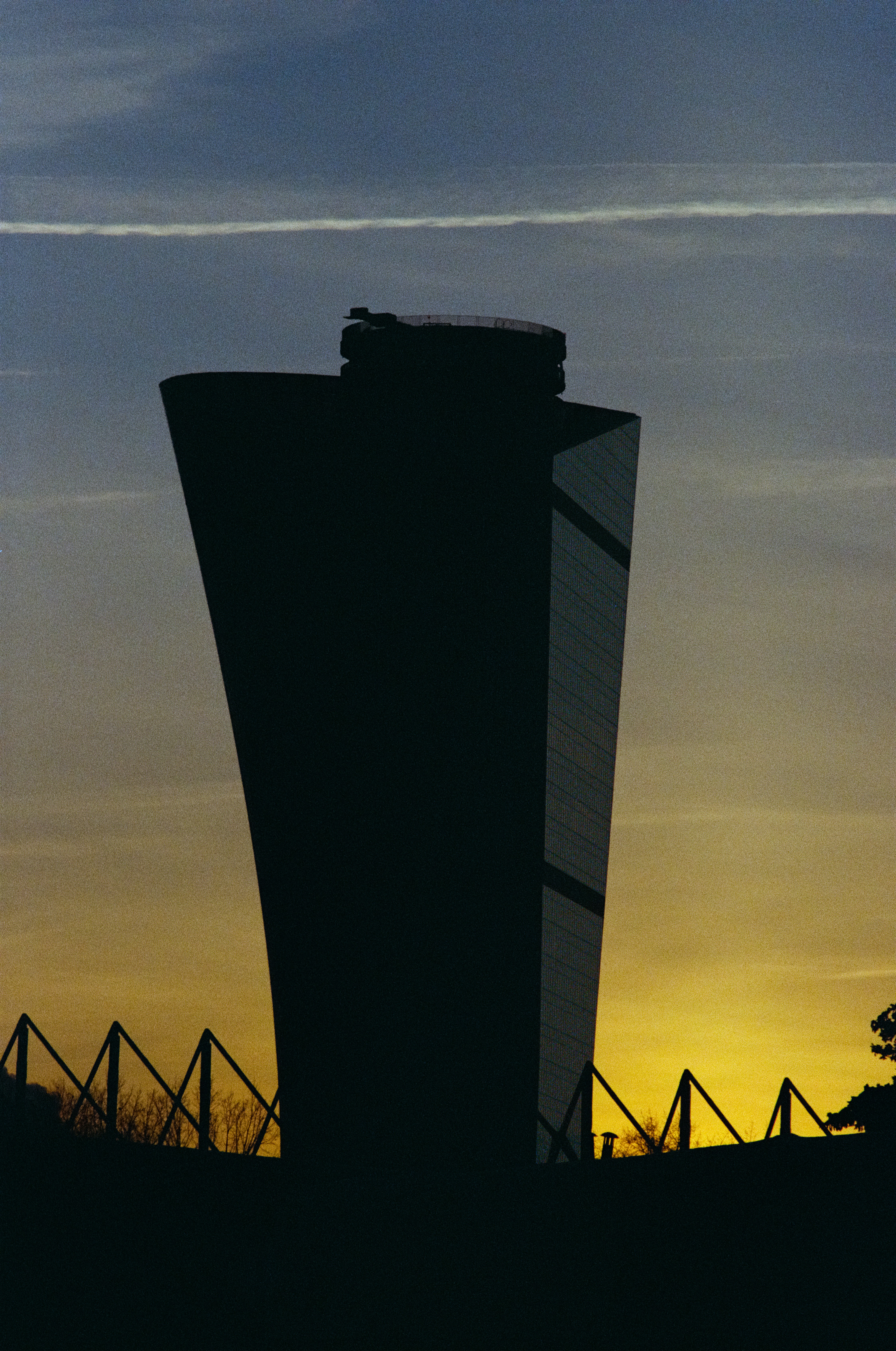 Silhouette of a modern skyscraper against a golden sunset sky with a contrail trace. Minimalist urban architecture. Film: ISO 400 (+2 stops push) | Lens: Takumar 200mm f/4.0