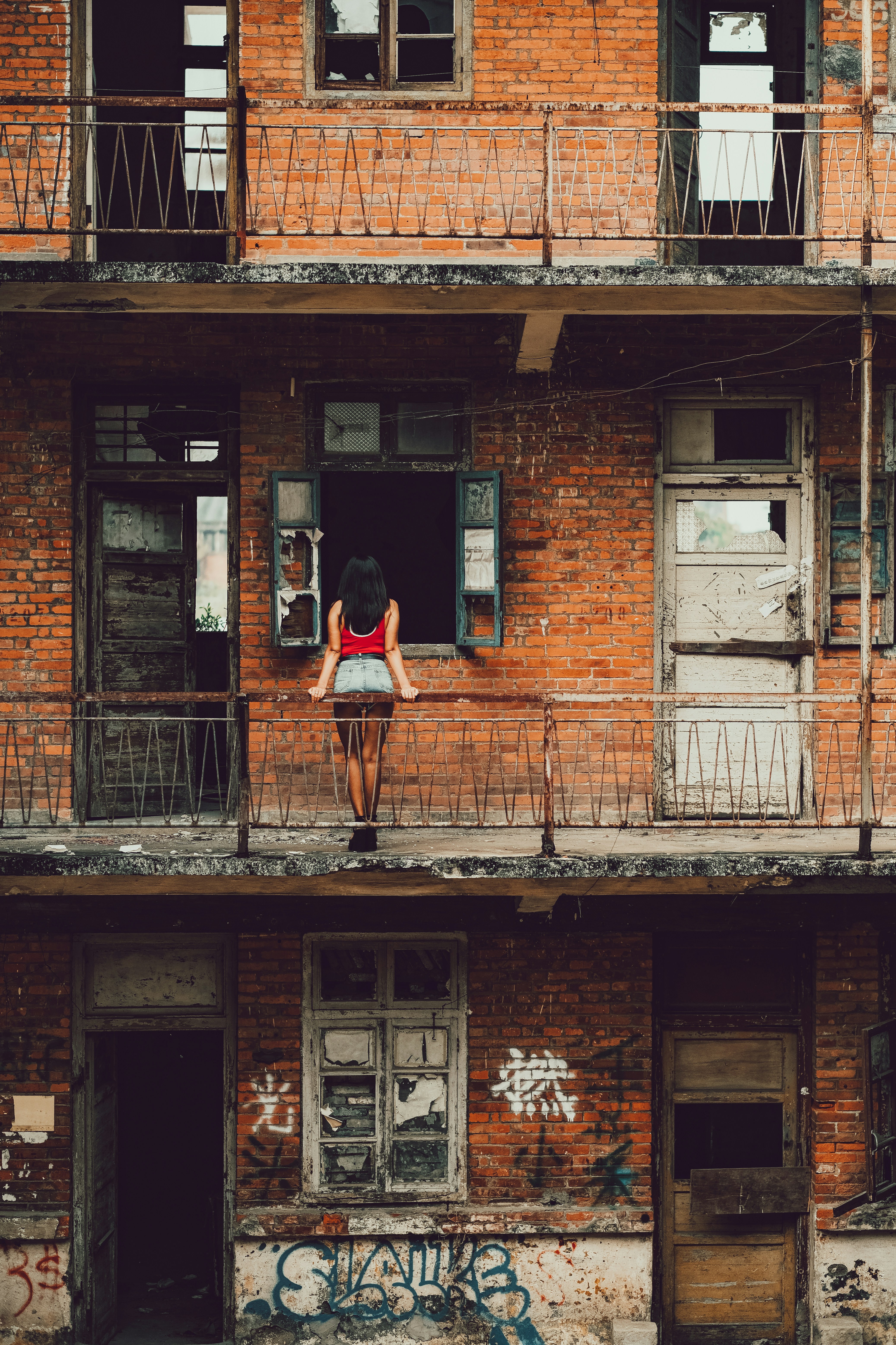 Balcony Quiet: A solitary figure in a decaying brick facade