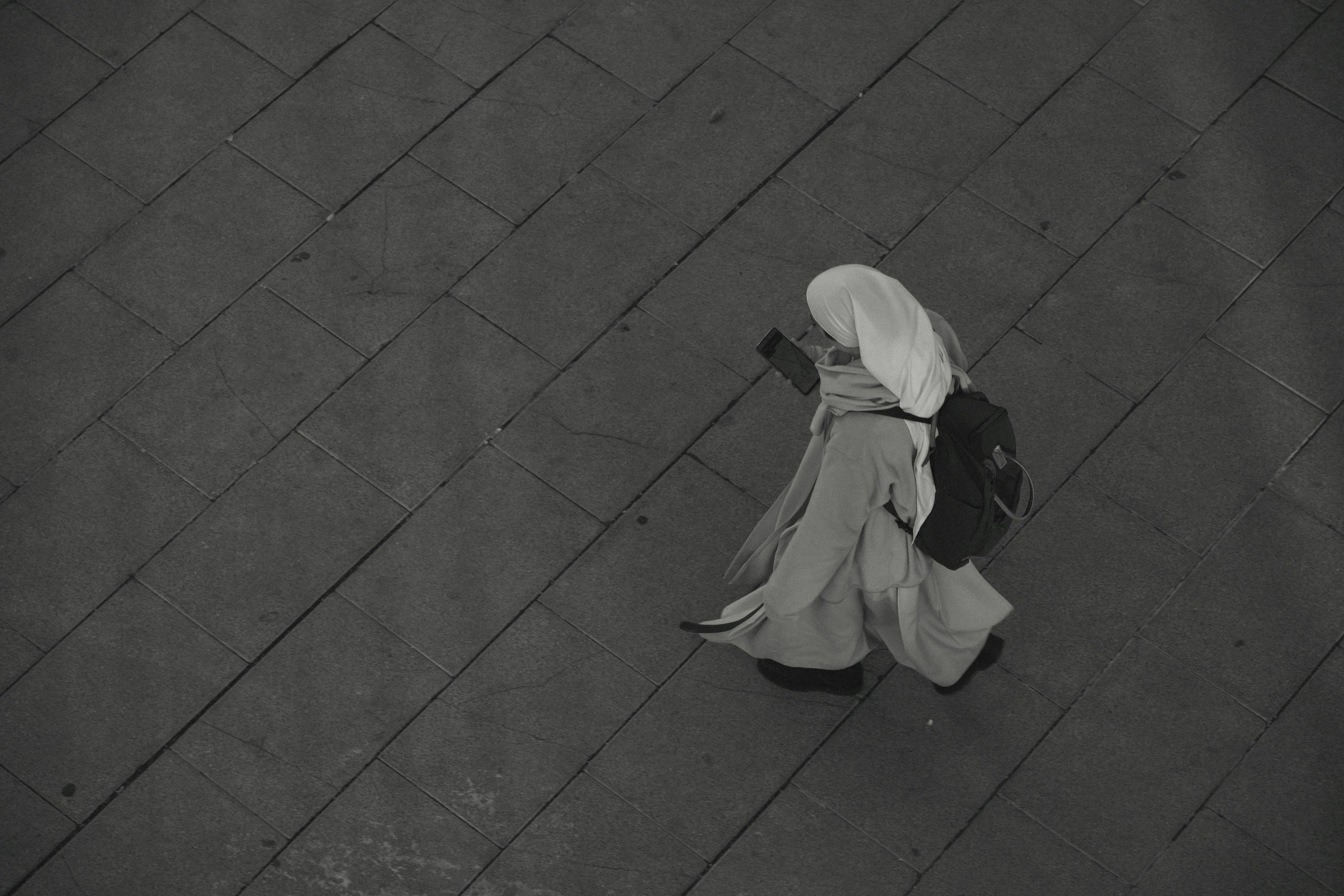 Wandering silhouette: a hooded figure crossing a paved plane