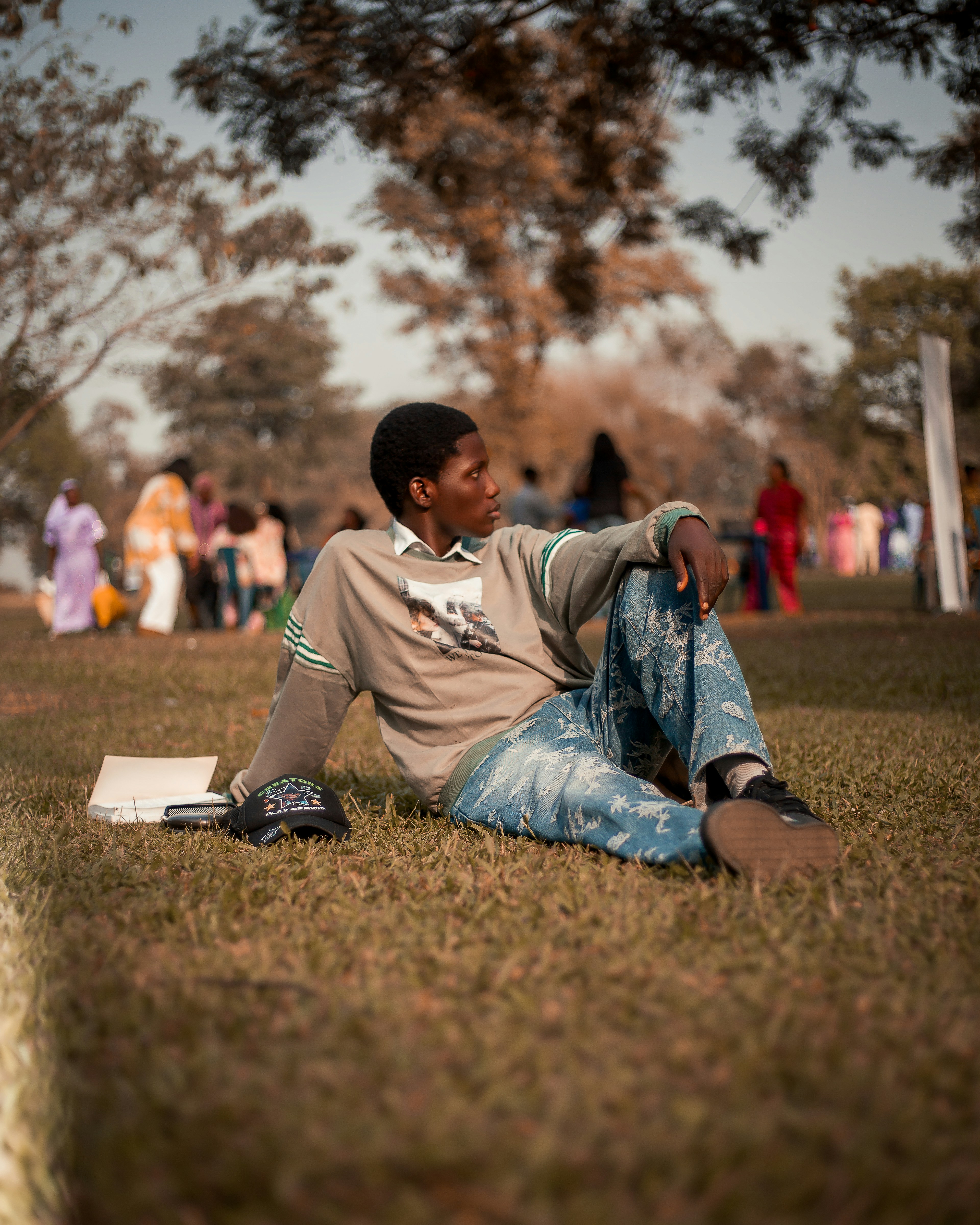 Lone youth in a sunlit park, a moment of quiet amid a distant crowd