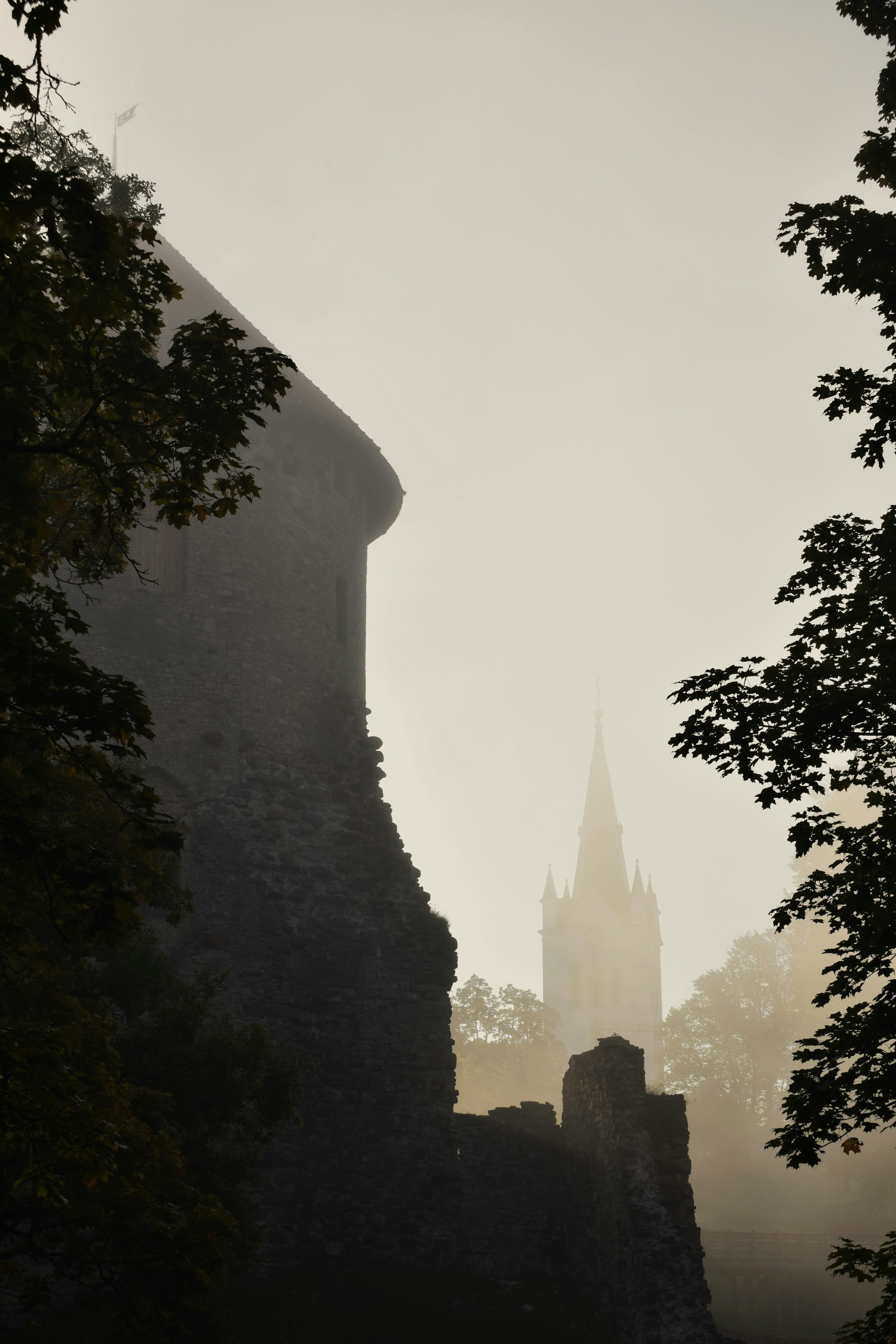 Morning silhouettes: a ruined tower and distant church spire through mist