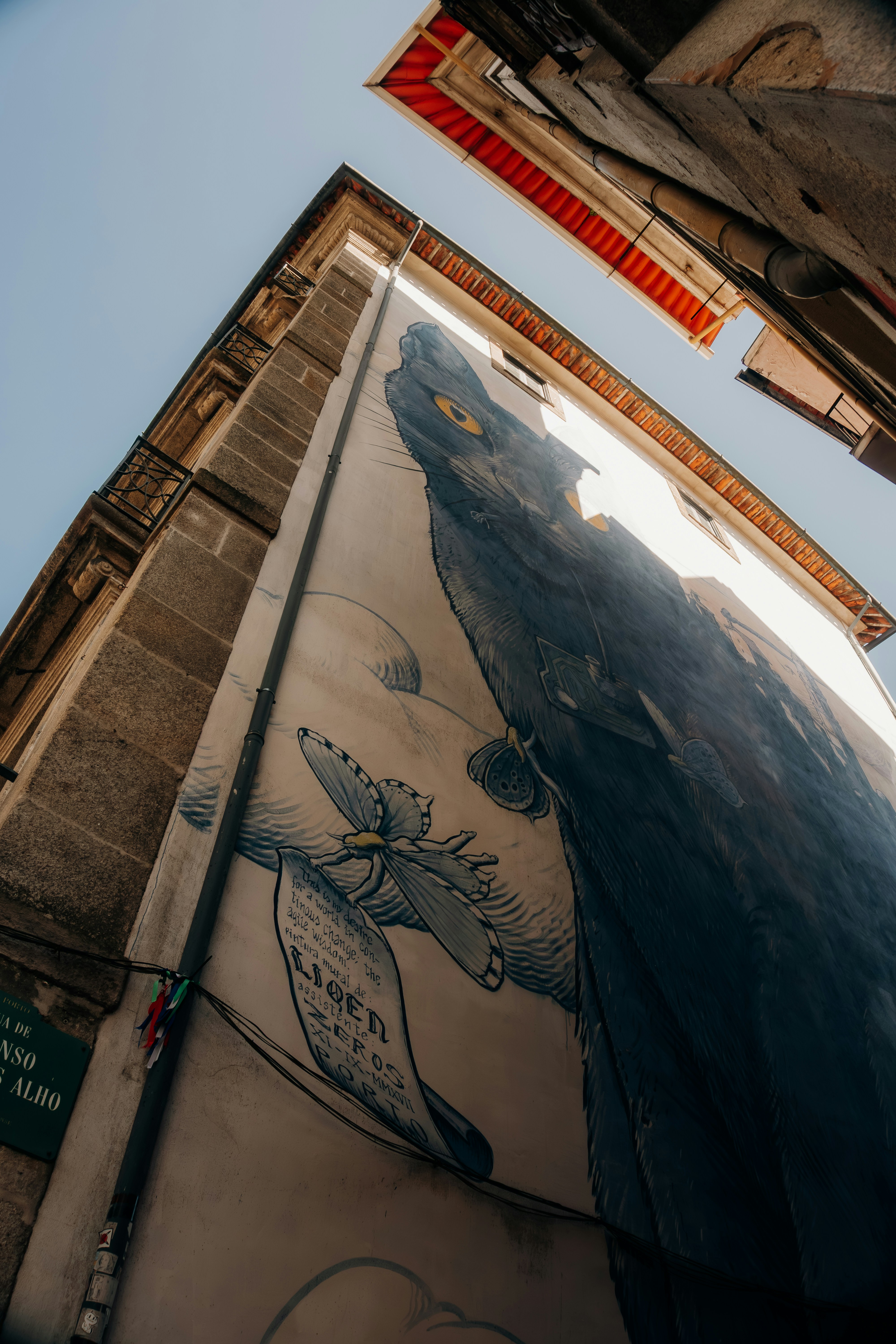 Tilted urban mural: a giant blue creature dominates a narrow alley