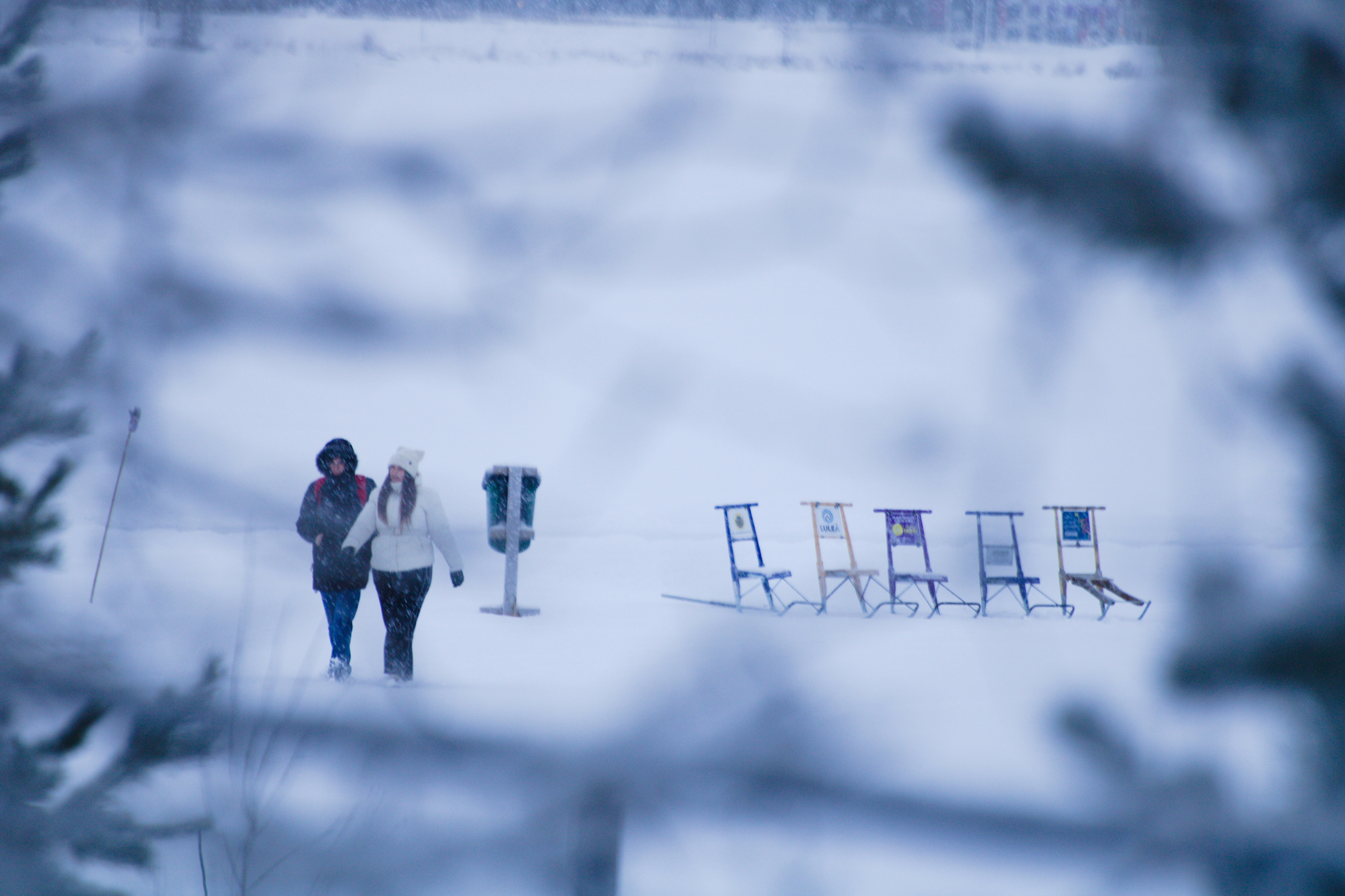 Winter Narrowness: A Couple Walks Through Snow Beside Empty Deck Chairs