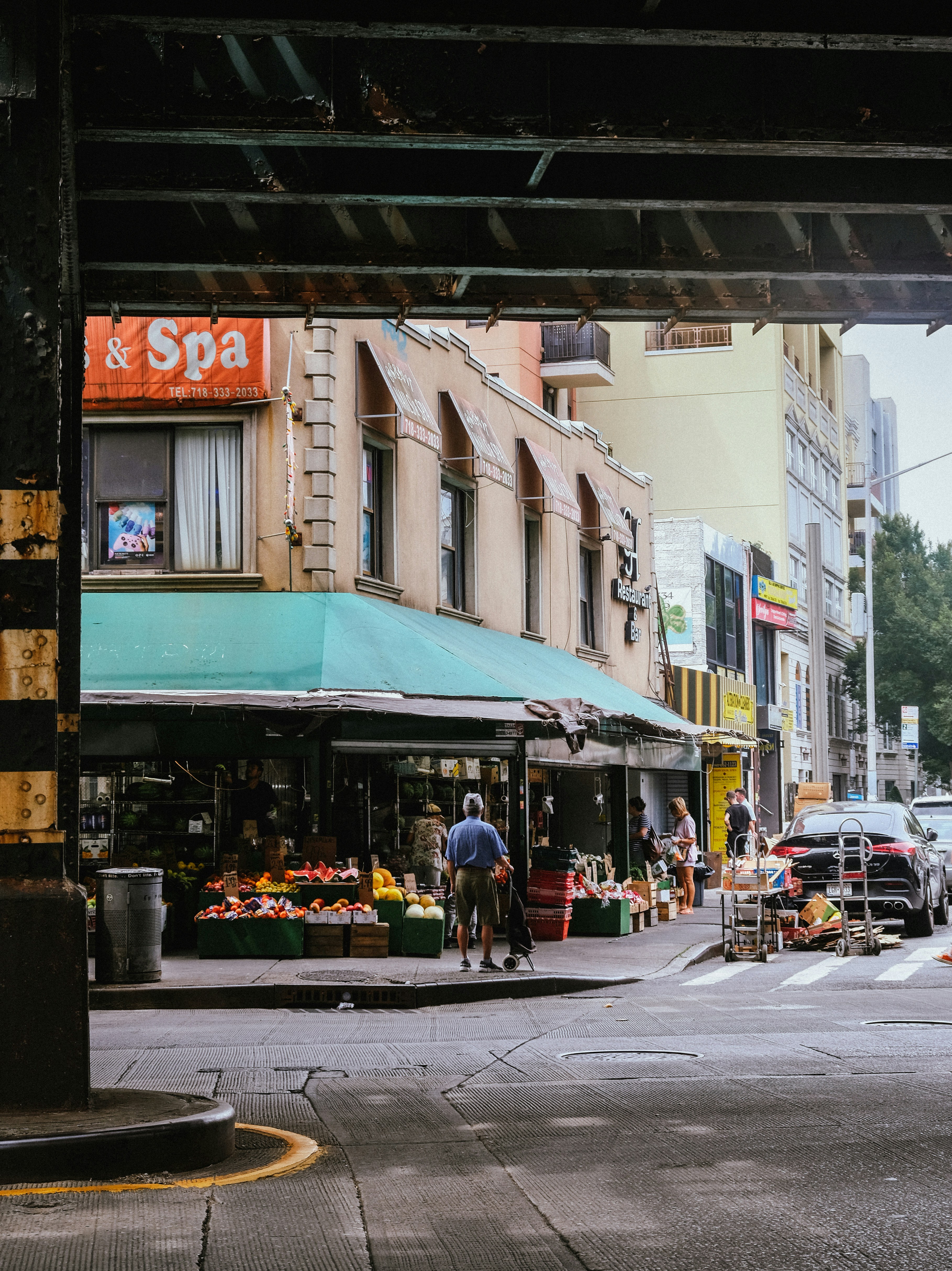 Urban Produce Walk: Street Market Beneath a Grim Iron Beam