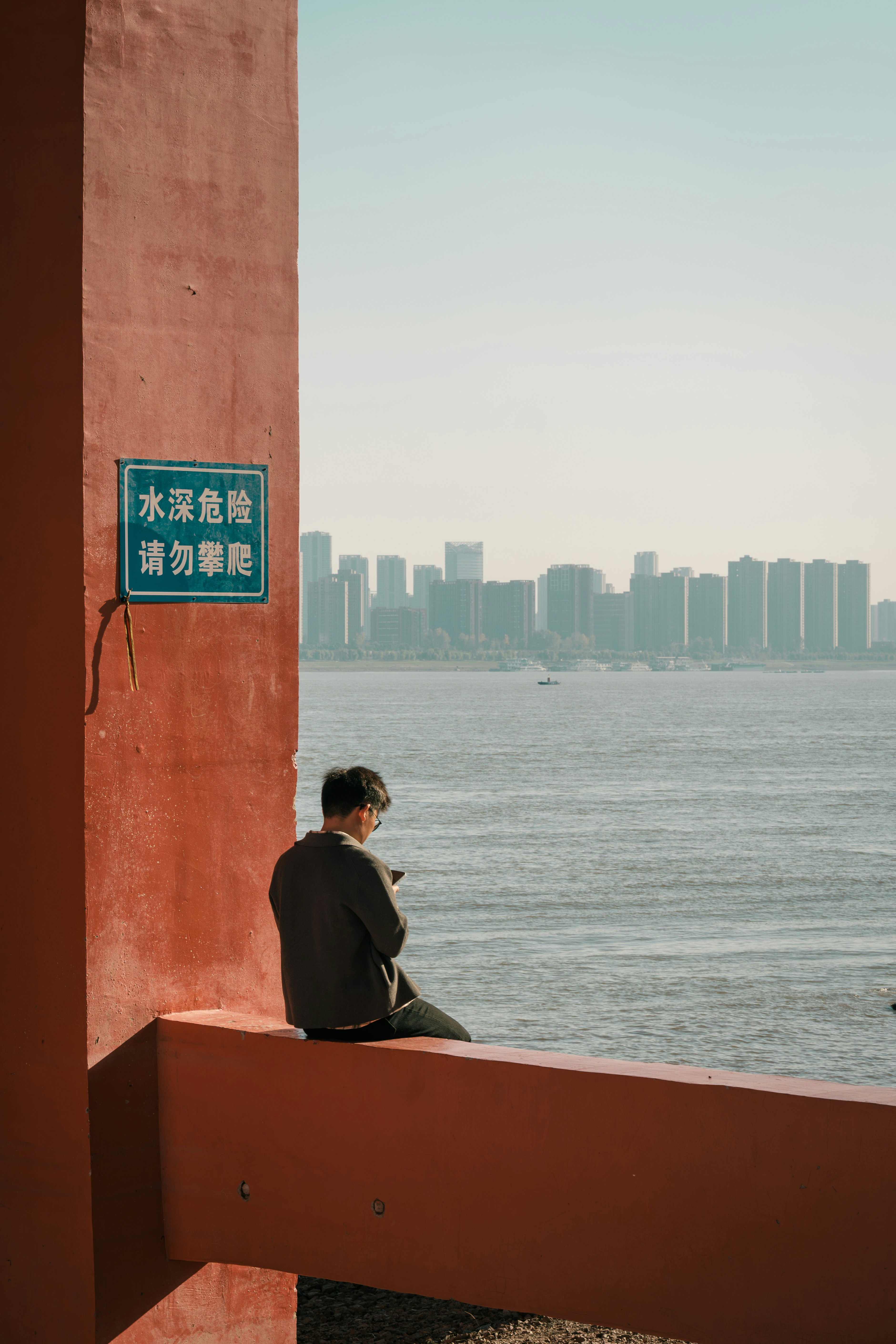 Seated Stature: A solitary observer by the red jetty overlooking a distant city