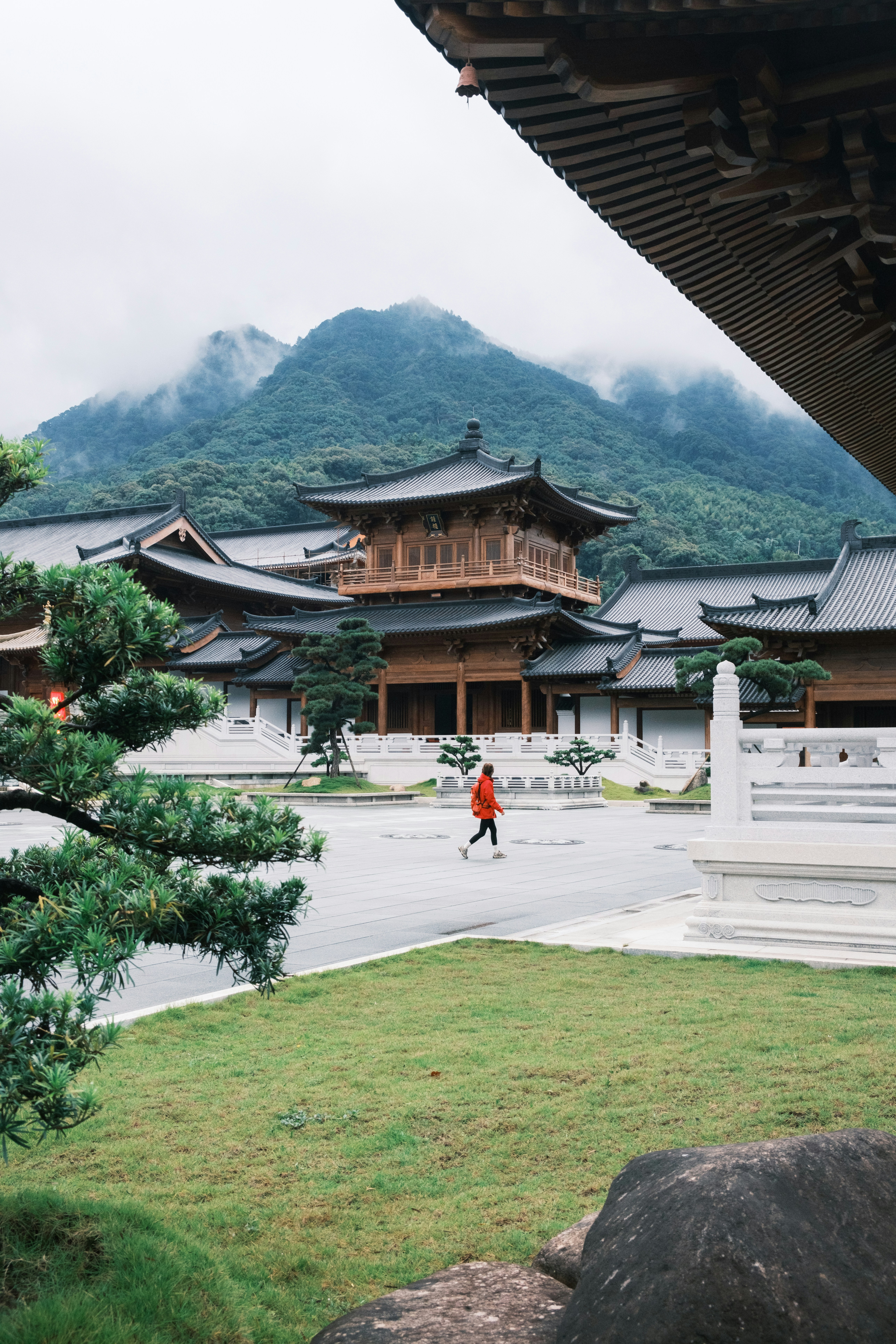 Red-cloaked Visitor Before a Traditional Pergola Amid Misty Mountains