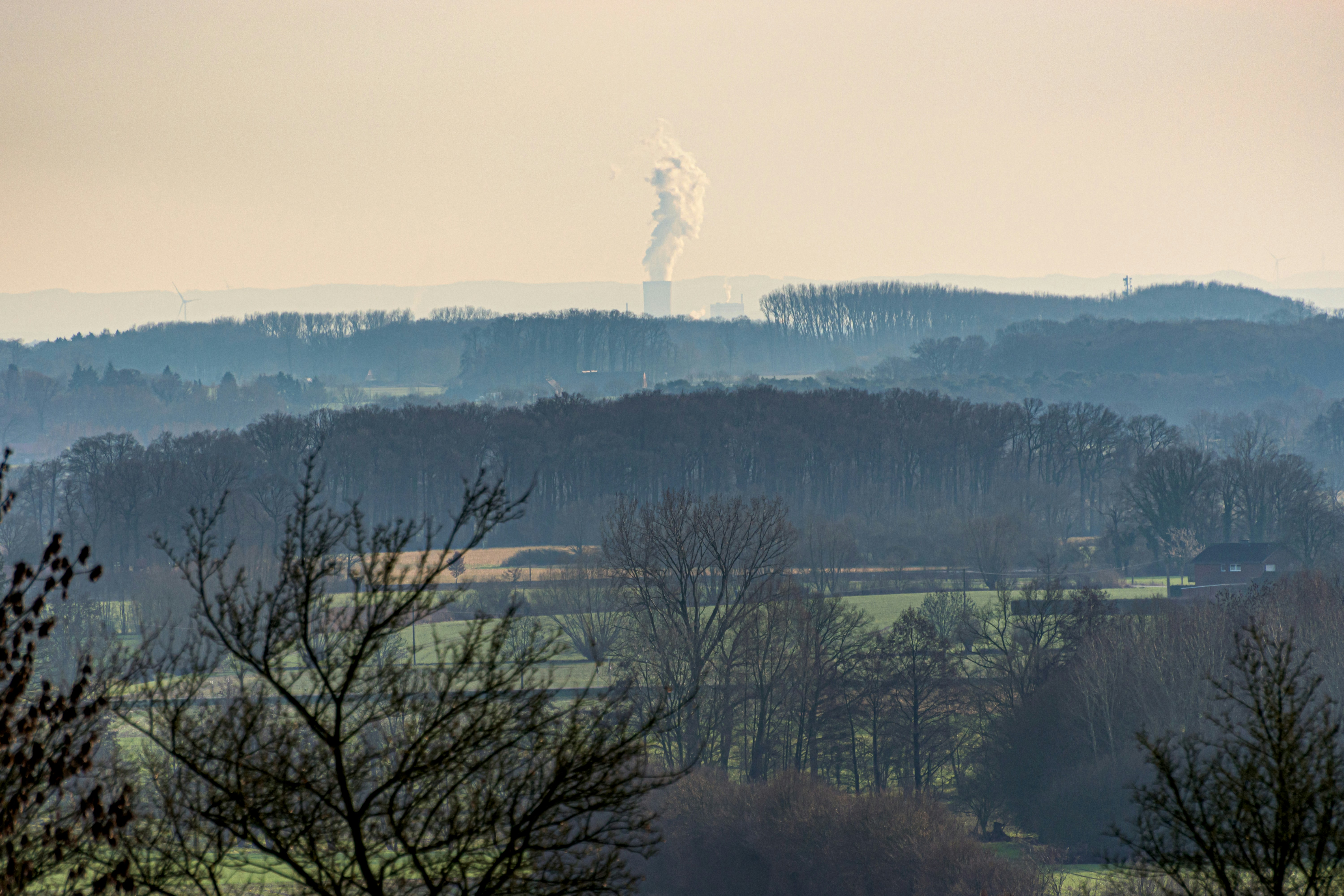 Industrial plume silhouette over rolling farmlands at dusk