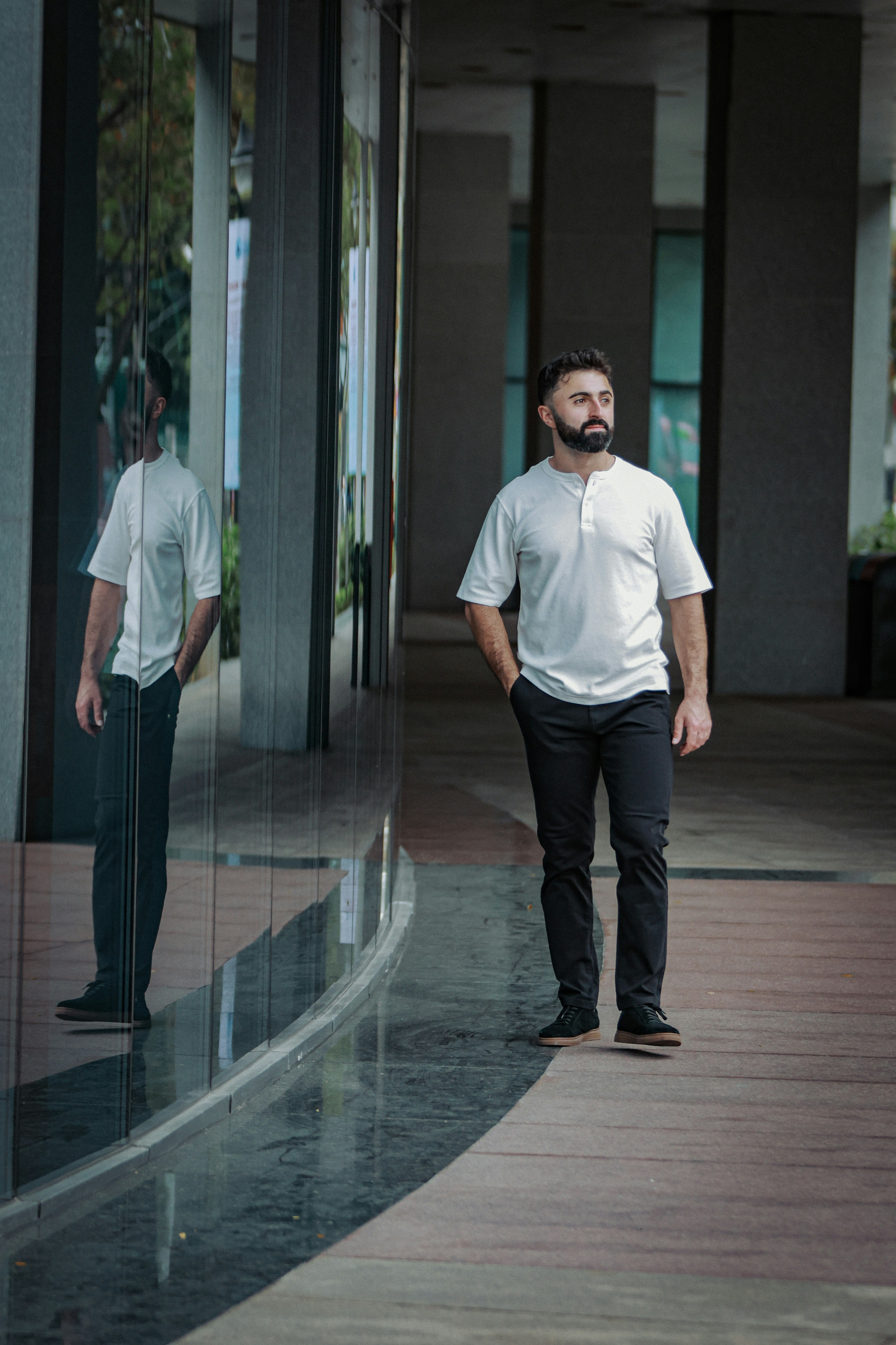 Man in white polo by a curved glass facade at a modern building entrance