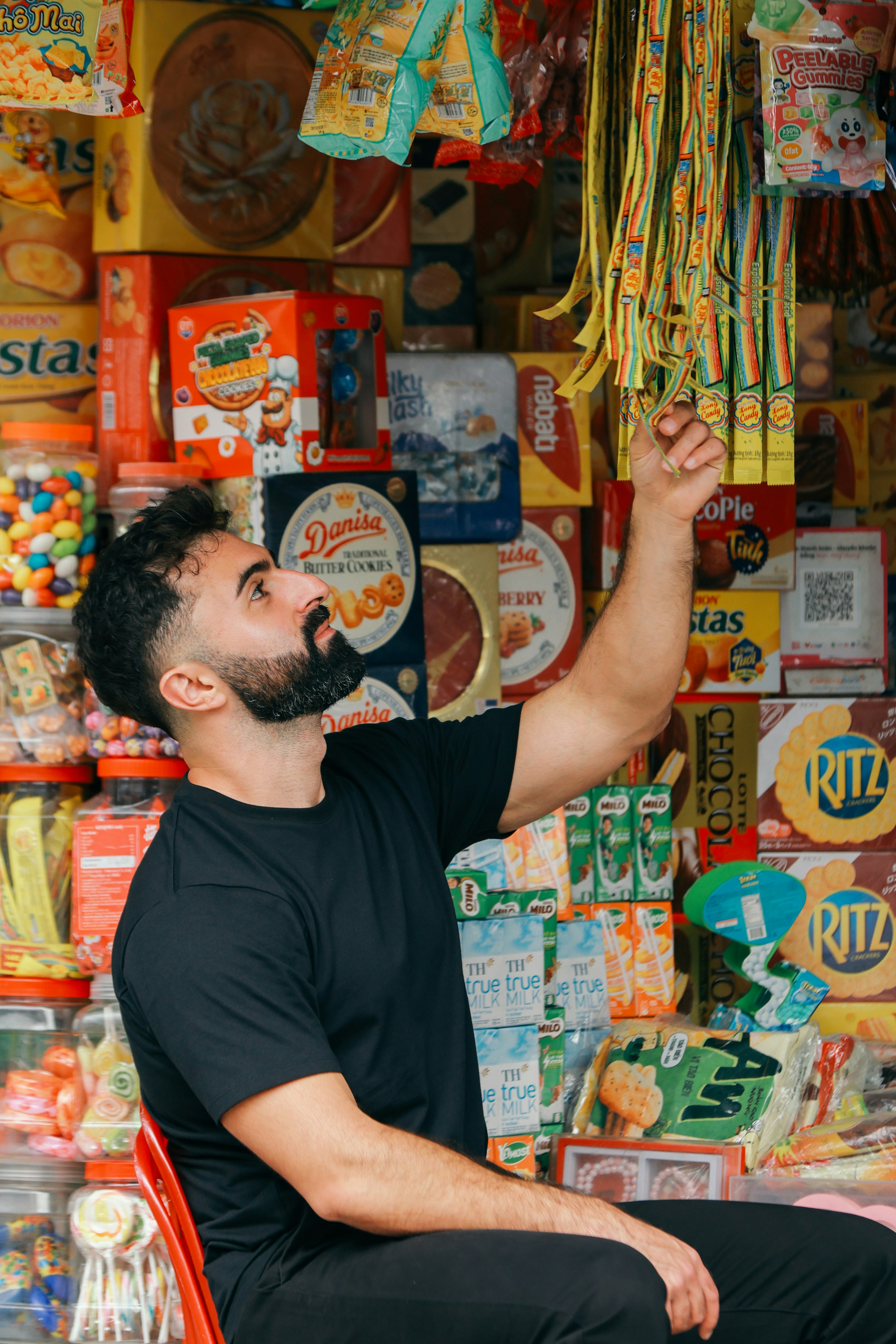 Man in a black shirt reaches for hanging candies amid a colorful shop display