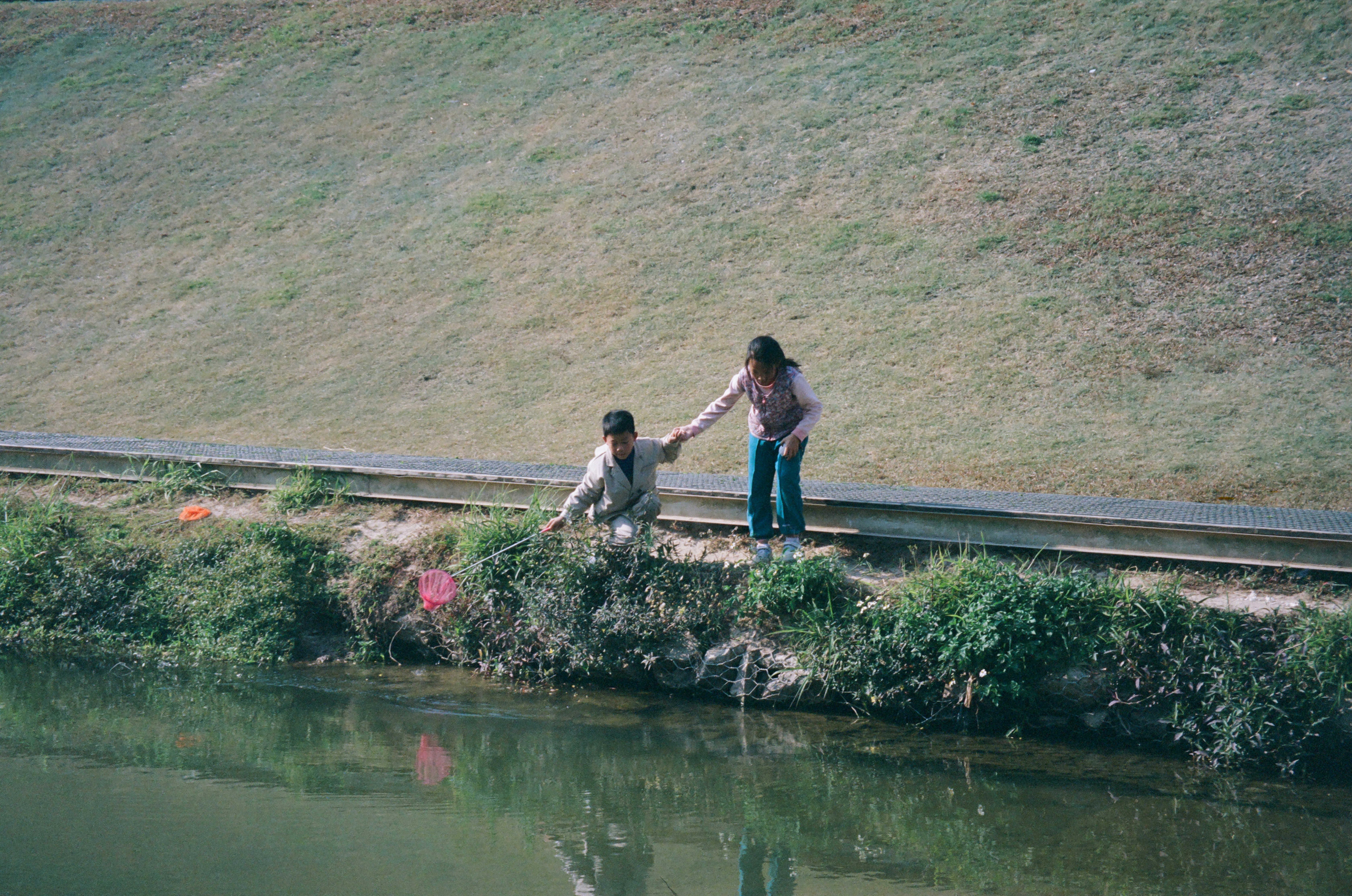Two Figures by the Canal: Lending a Hand Across the Water