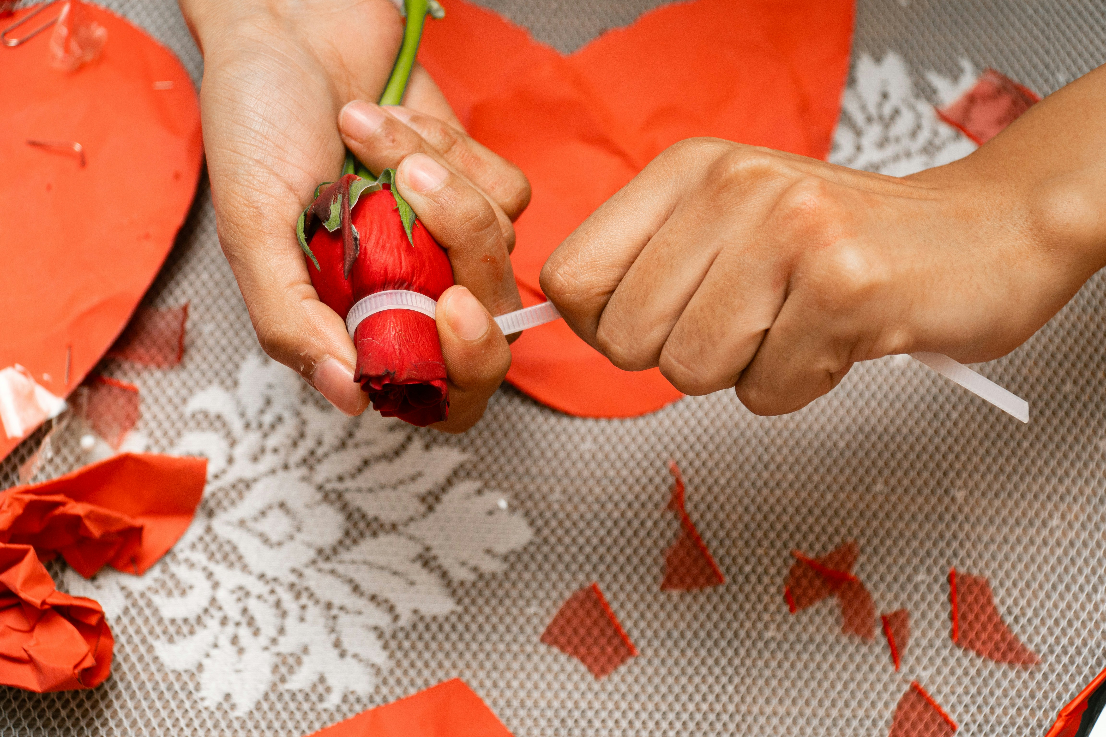 Hands at Work: Crafting a Red Rose with Scattered Tissue Confetti
