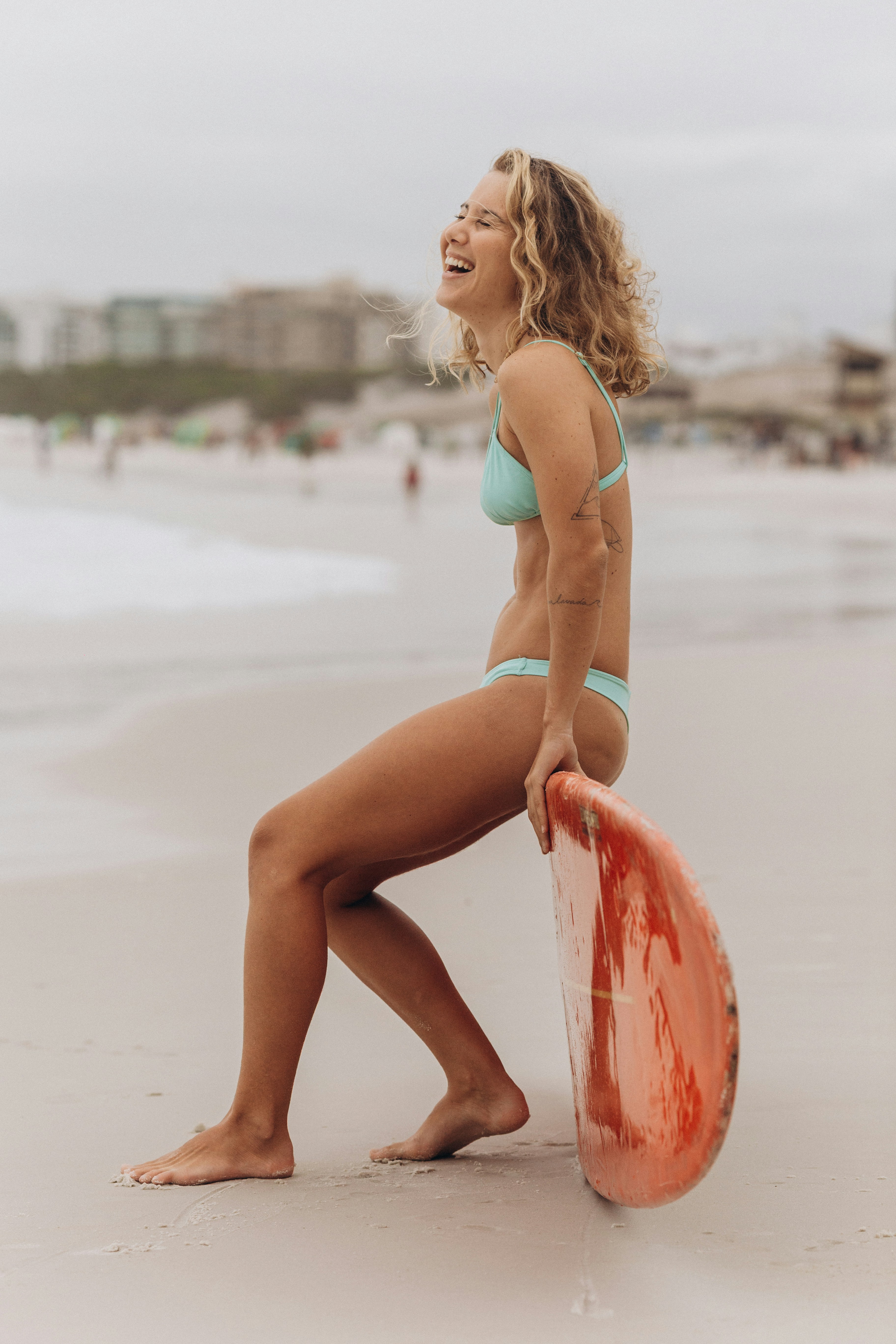 Laughing surfer in turquoise bikini with red board on sunlit beach
