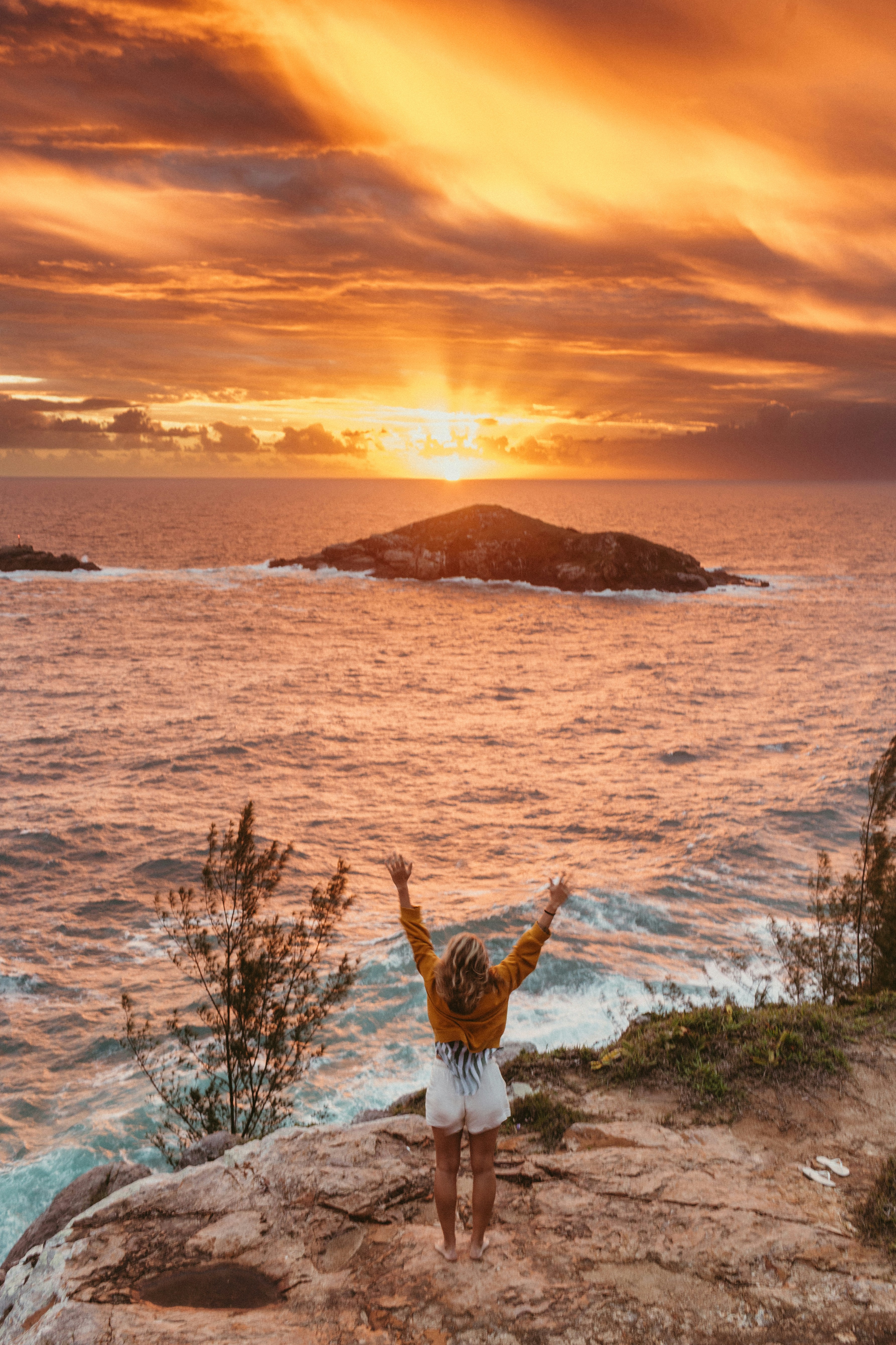 Sunset at the Edge: Raised Arms on a Cliff Overlooking a Golden Sea