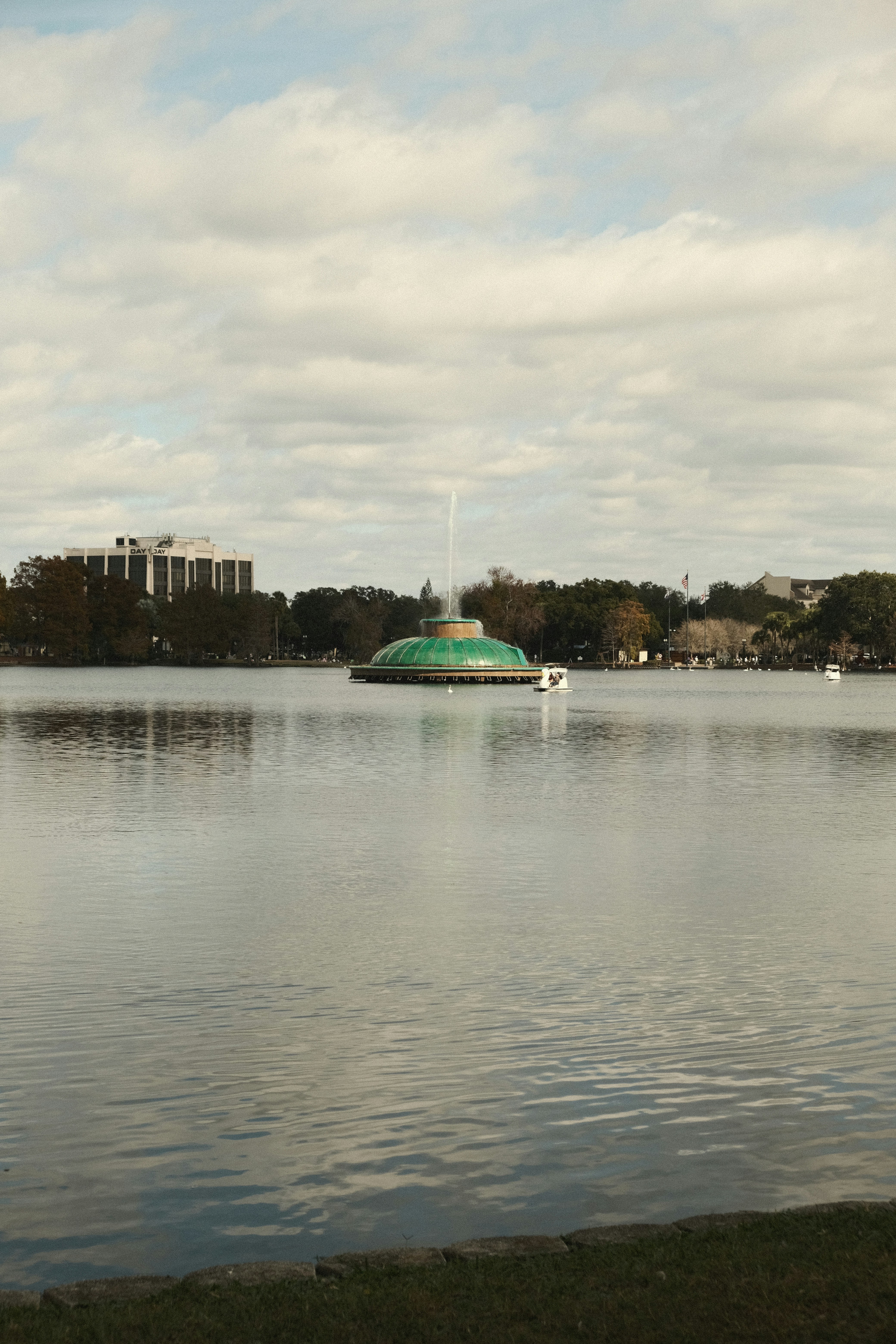 Green-topped fountain near the distant shoreline across a calm lake