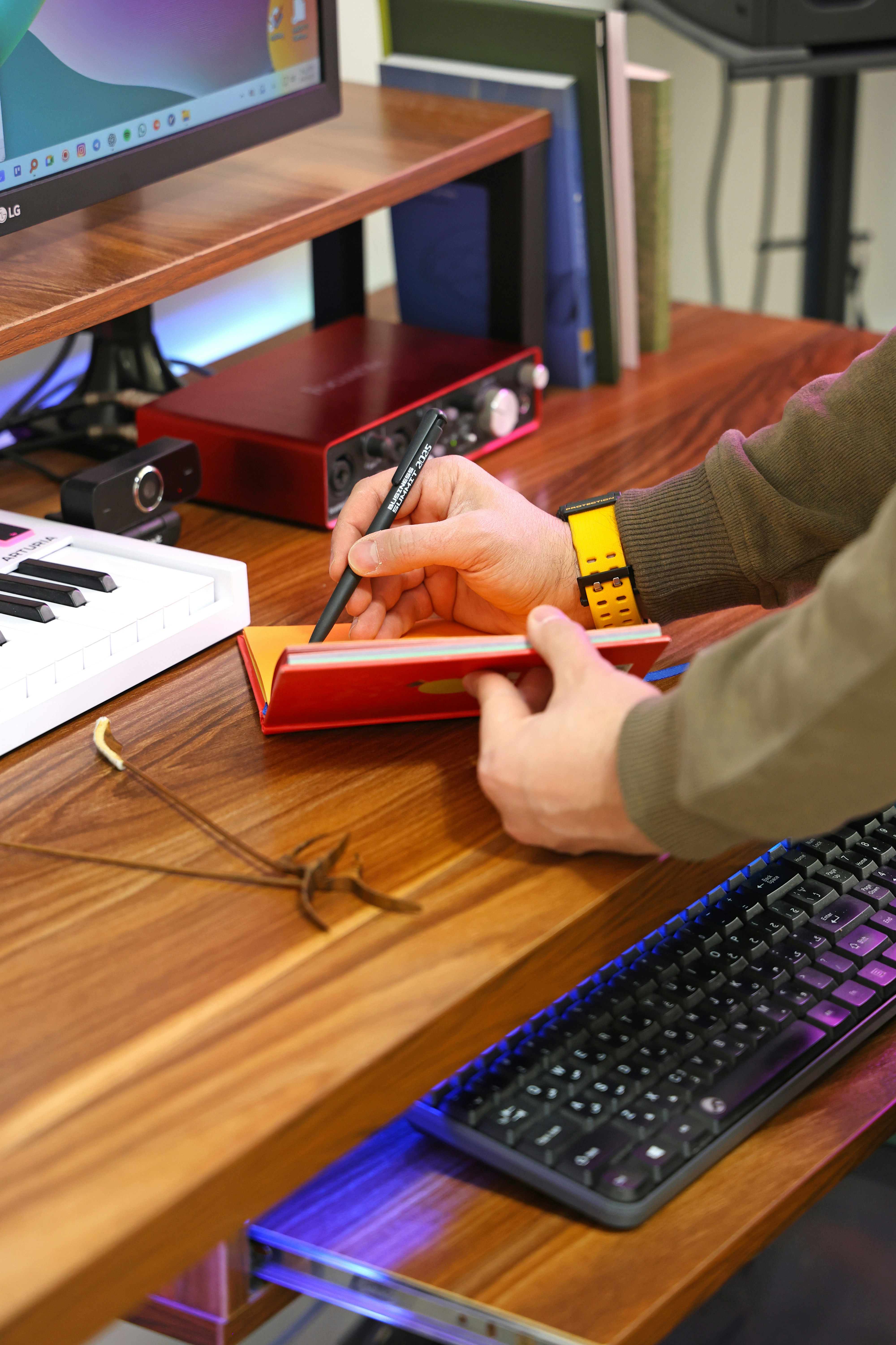 Handheld Creation: Writing Notes on a Red Notebook at a Tech Desk