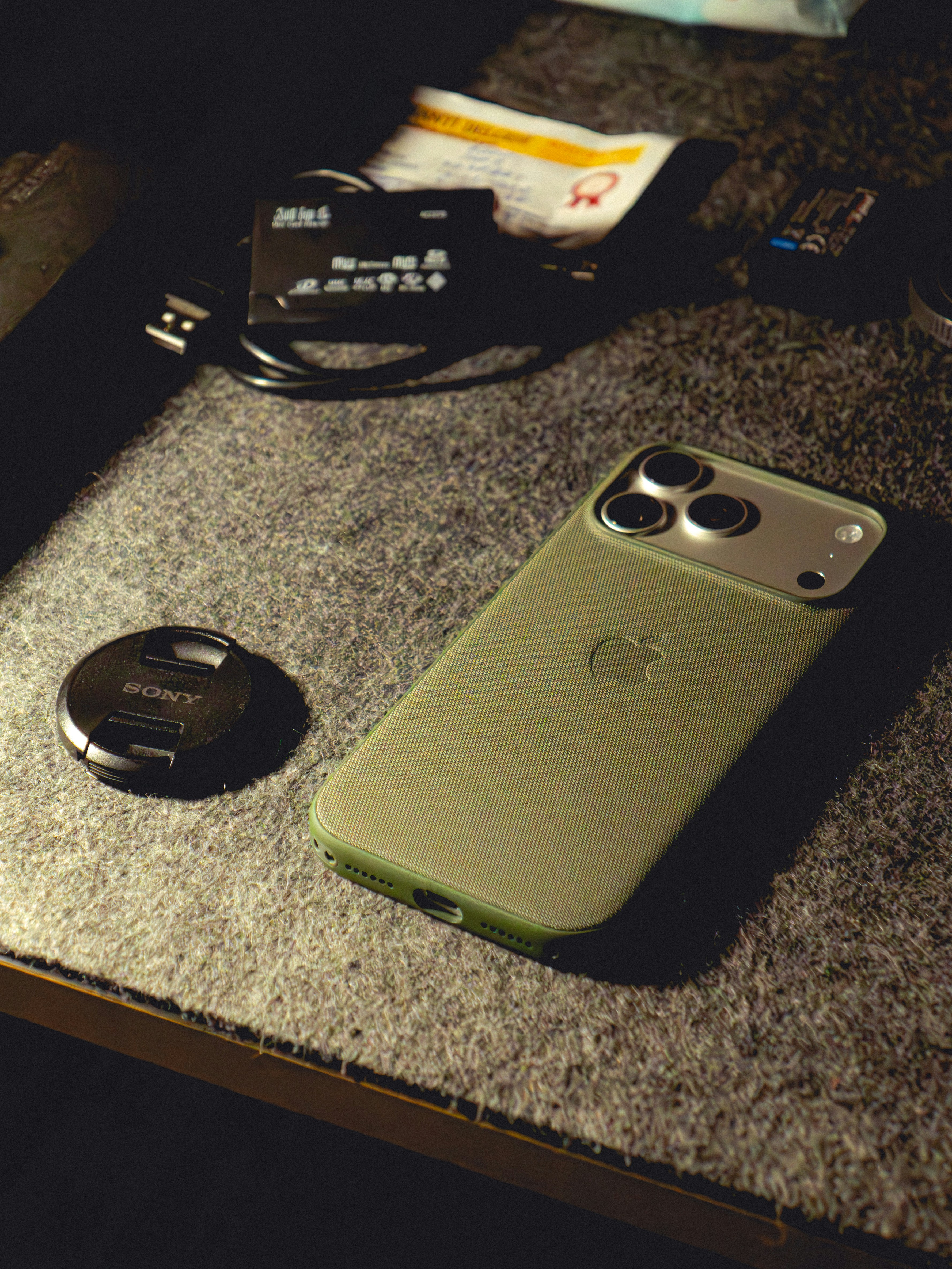 Olive Glass: A minimal desk scene with a green iPhone Pro resting beside a lens cap