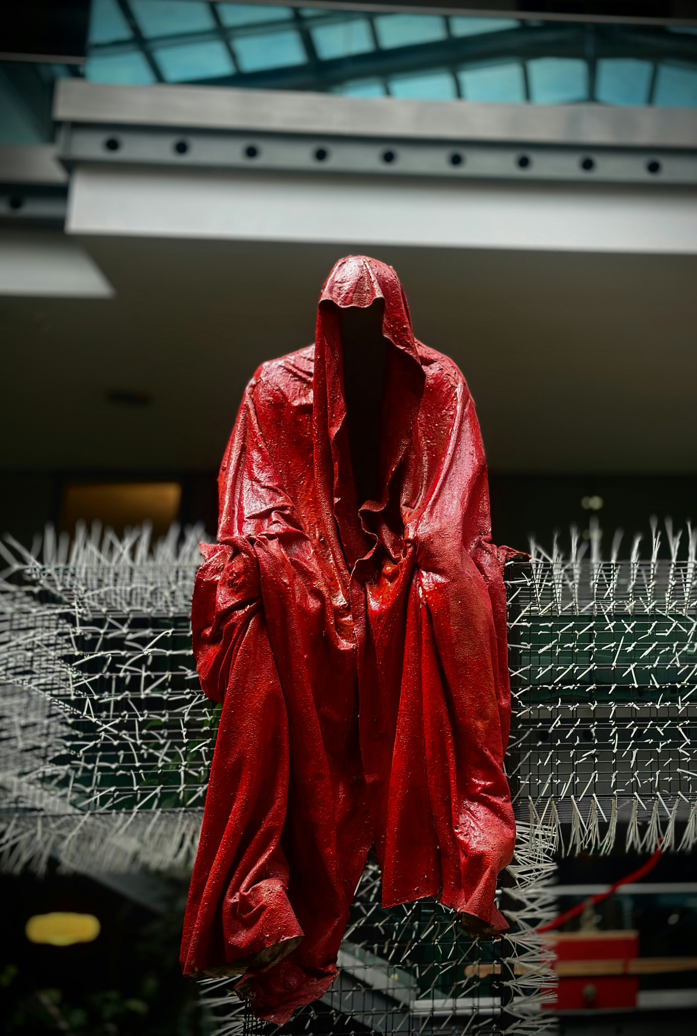 Red Cloaked Figure Suspended Over Spiky Barrier in an Atrium