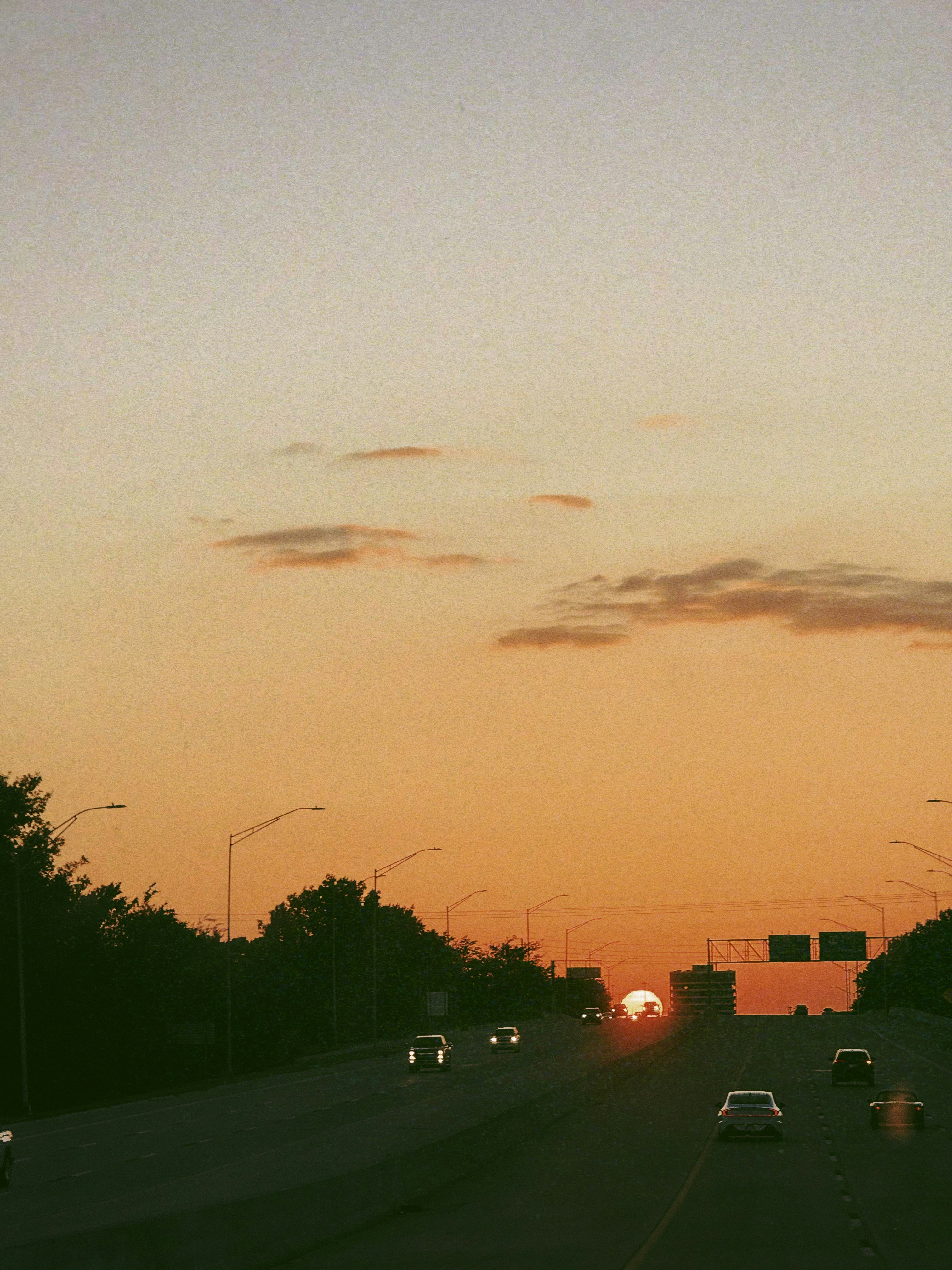 Sun-setting sky colors over a multi-lane highway as traffic fades in the distance; the scene emphasizes calm, warm tones and a horizon glow.