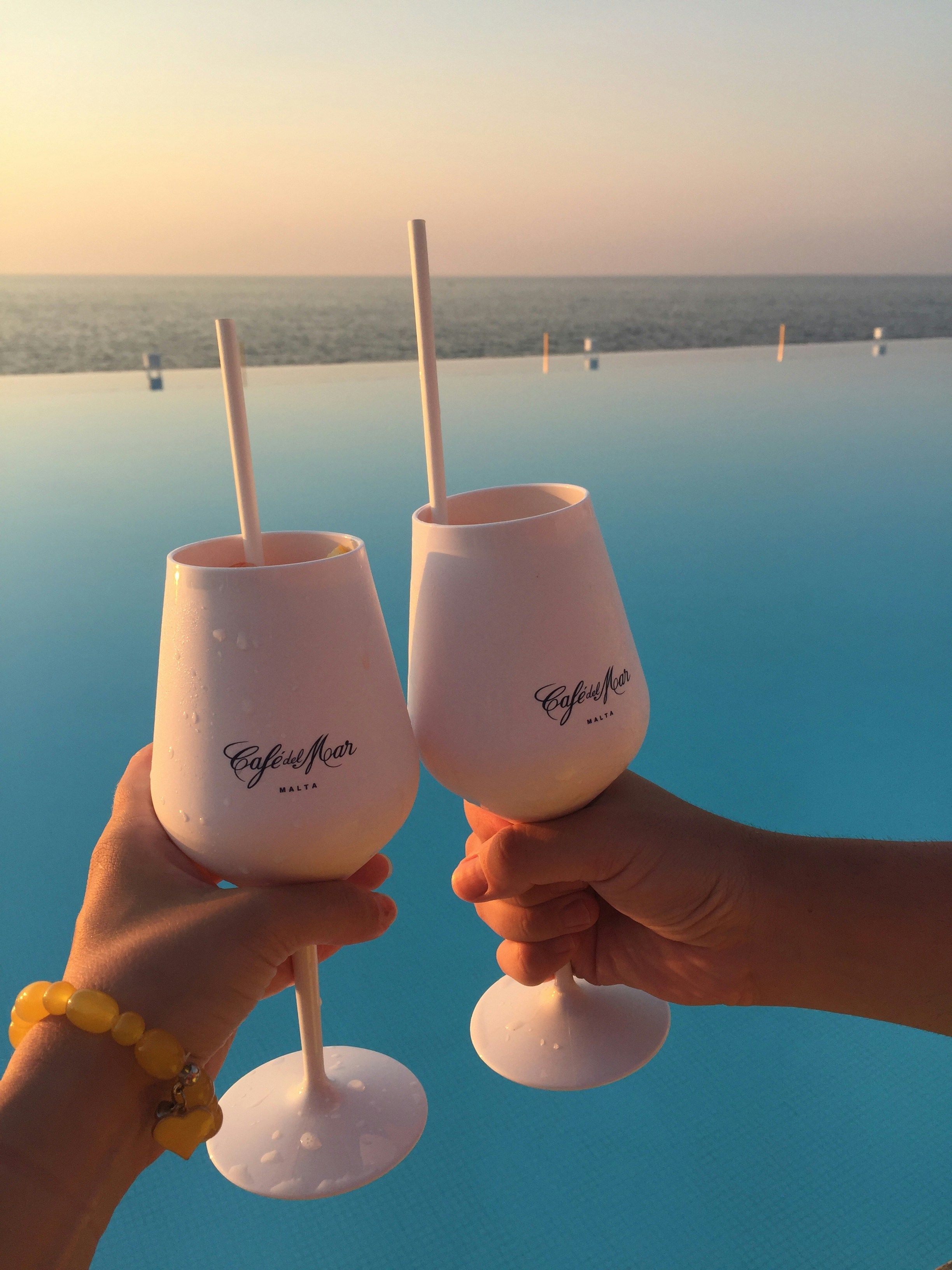 Two Glasses Raise a Sunset Toast Over an Infinite Pool