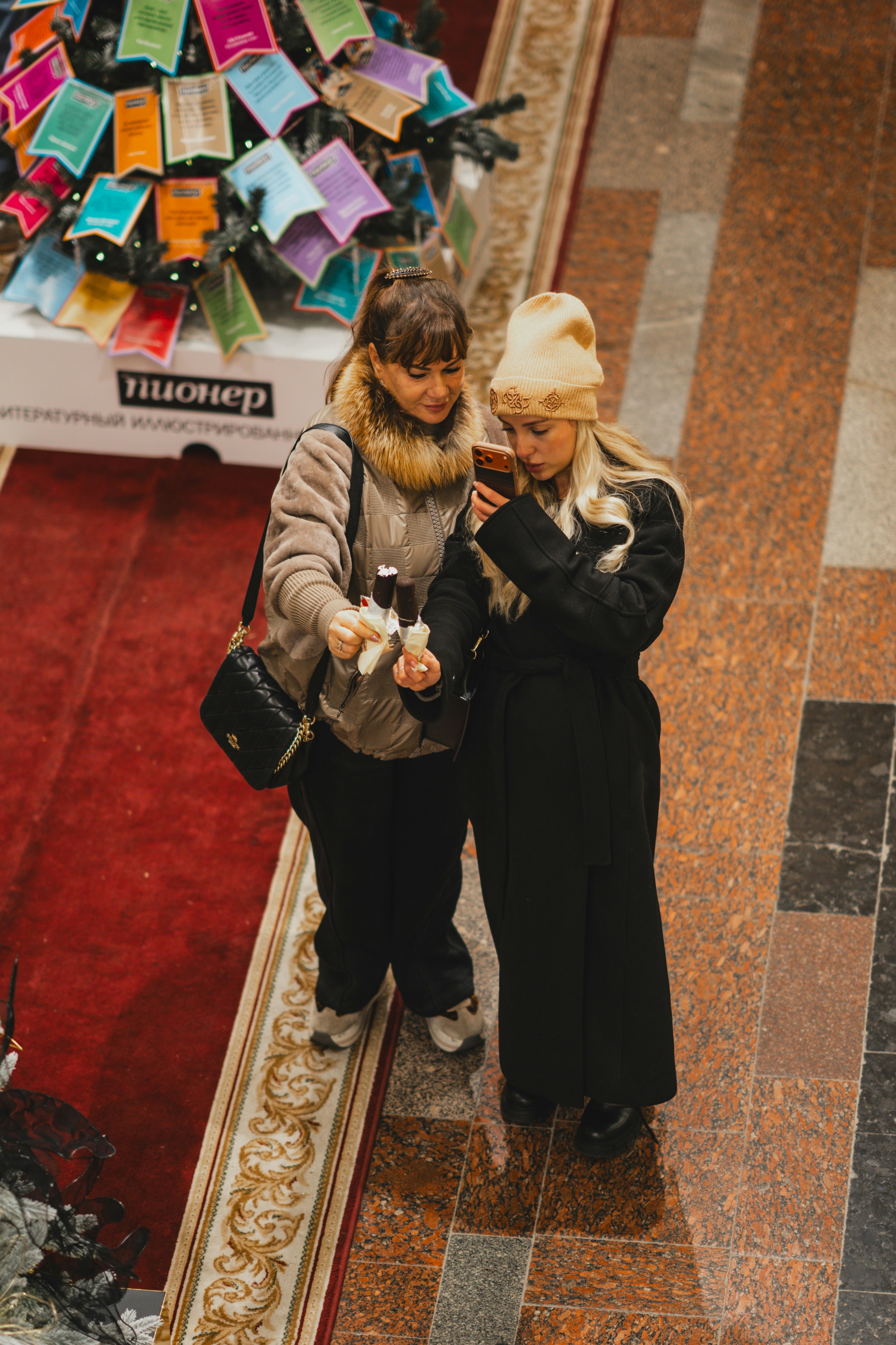 Two women on a carpeted aisle examining items against a colorful wall display