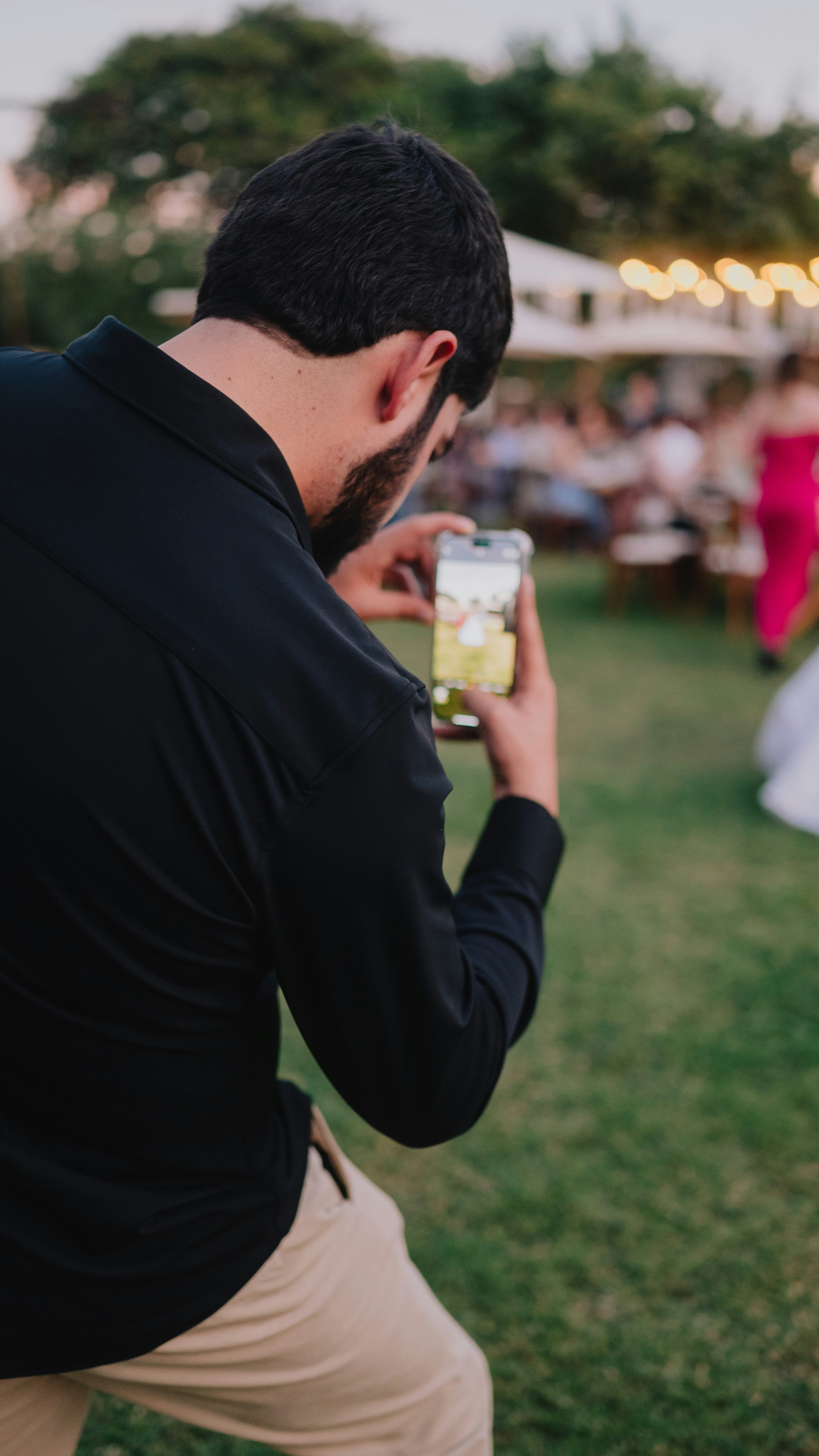Grove of moments: A guest captures a shared smile with a phone at a garden reception