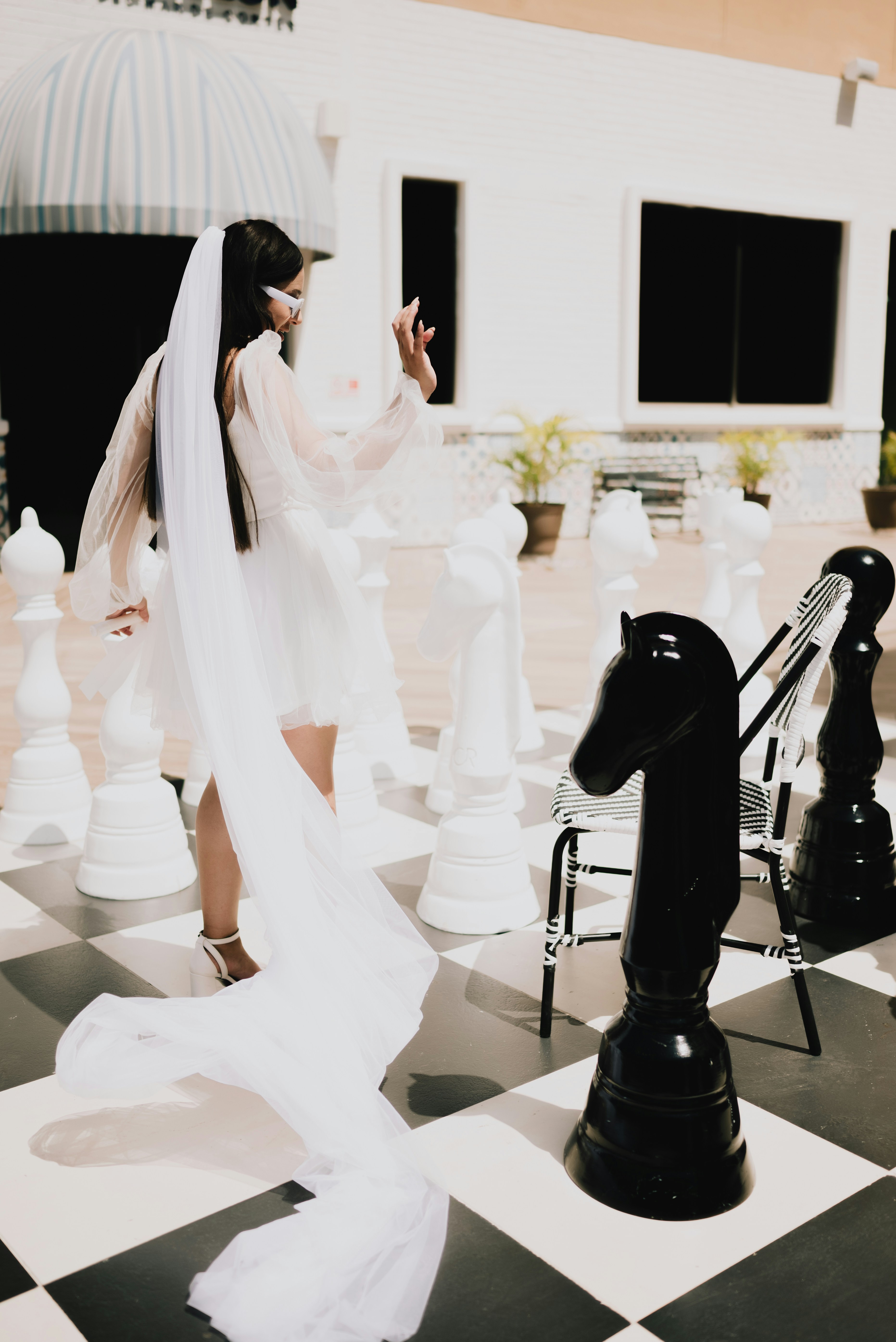 Bride in White Surrounded by Life-Sized Chess in a Sunlit Courtyard