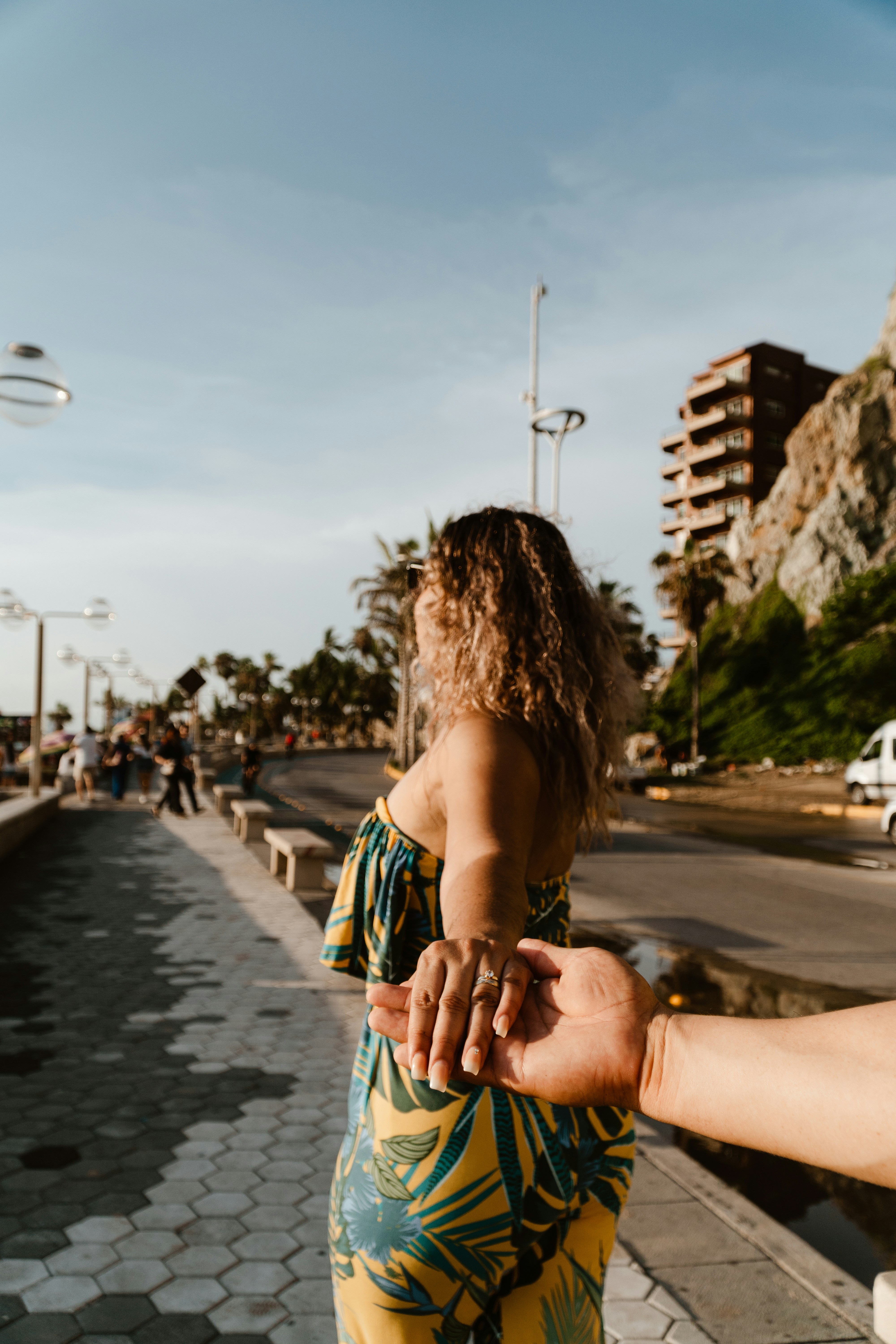 Woman leading man along a sunny seaside promenade.