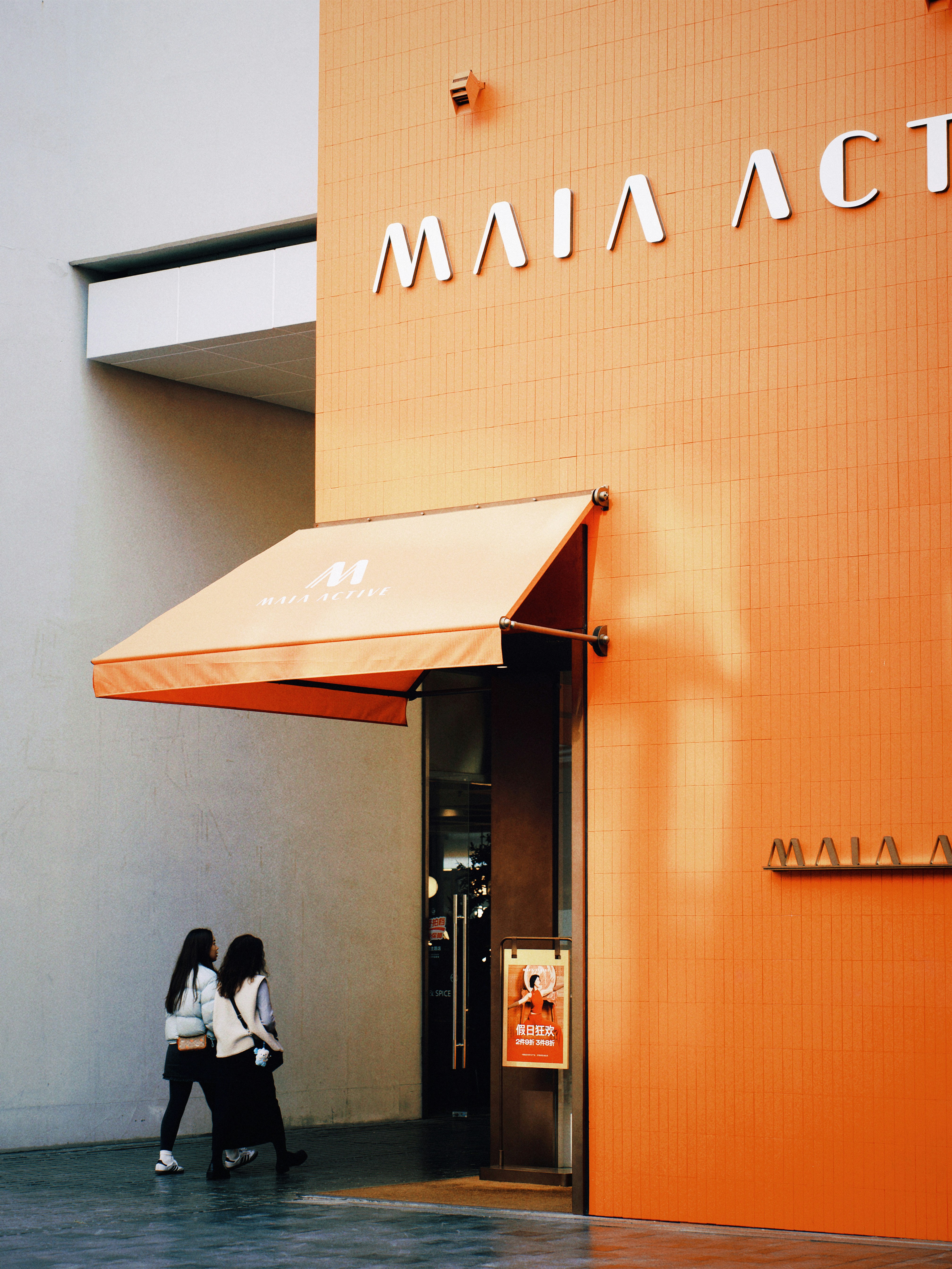 Orange Facade Gate: People Entering a Modern Storefront
