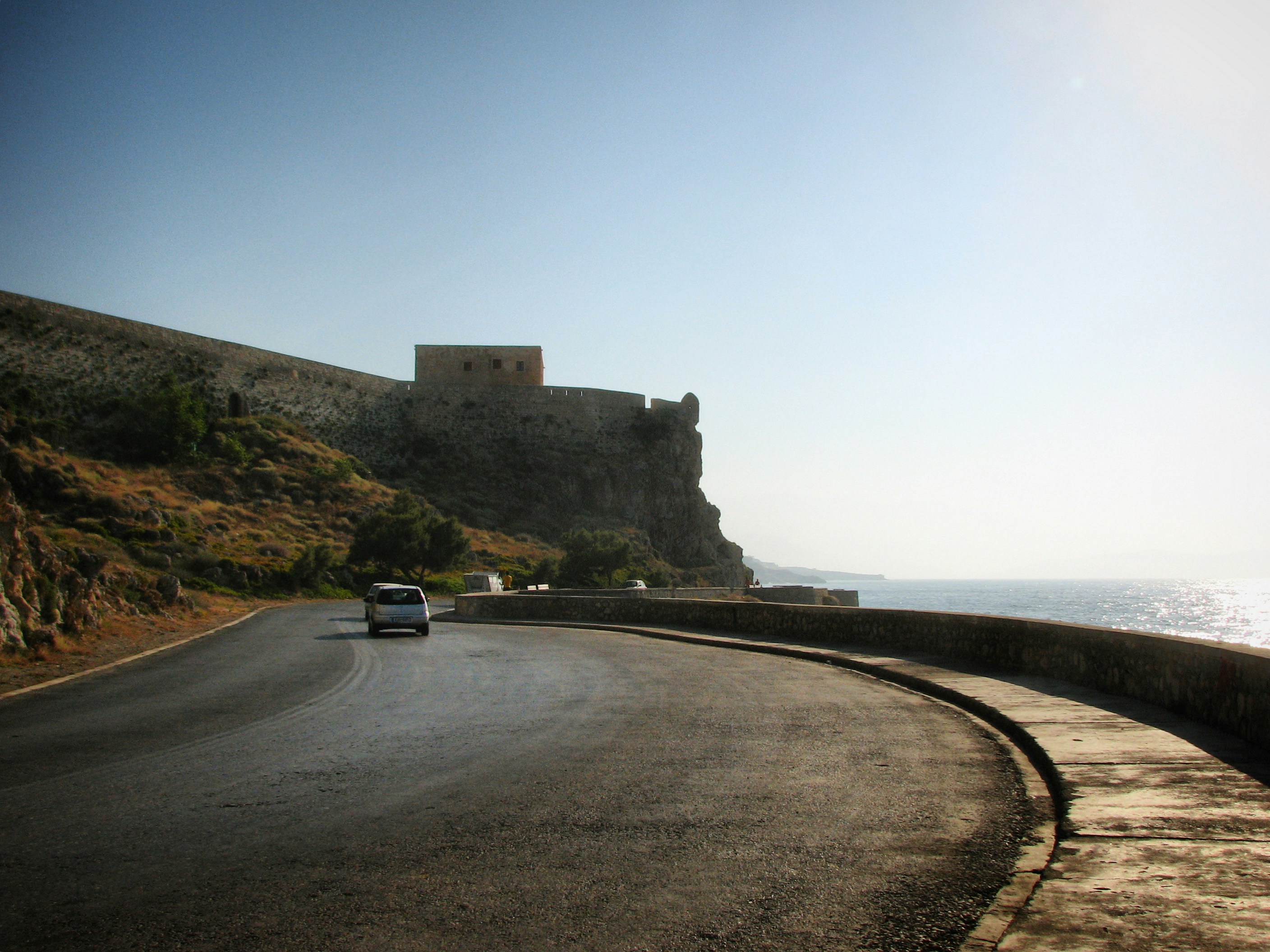 A car drives on a coastal road towards a fortress.
