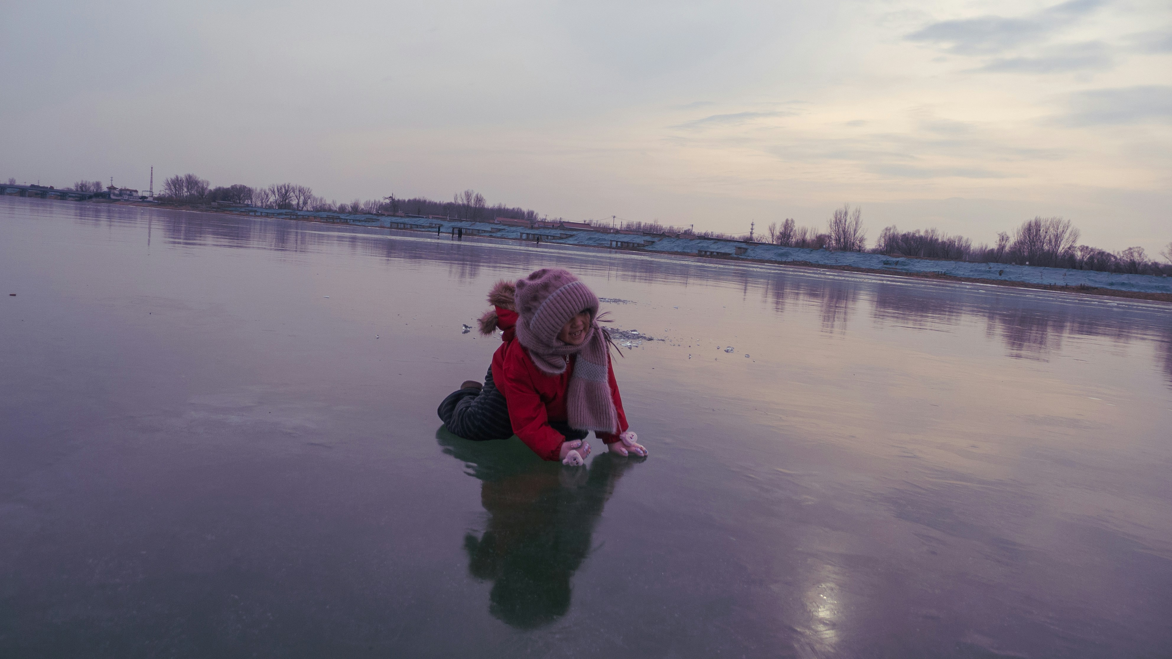 A person in a hijab kneels on a frozen lake.