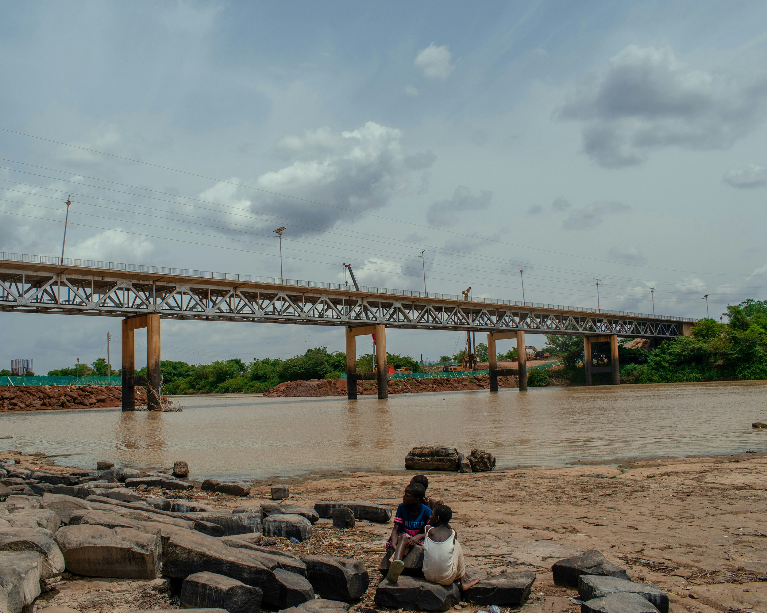 Riverside Bridge: Glisten of Brown Water and Kids by the Rocks