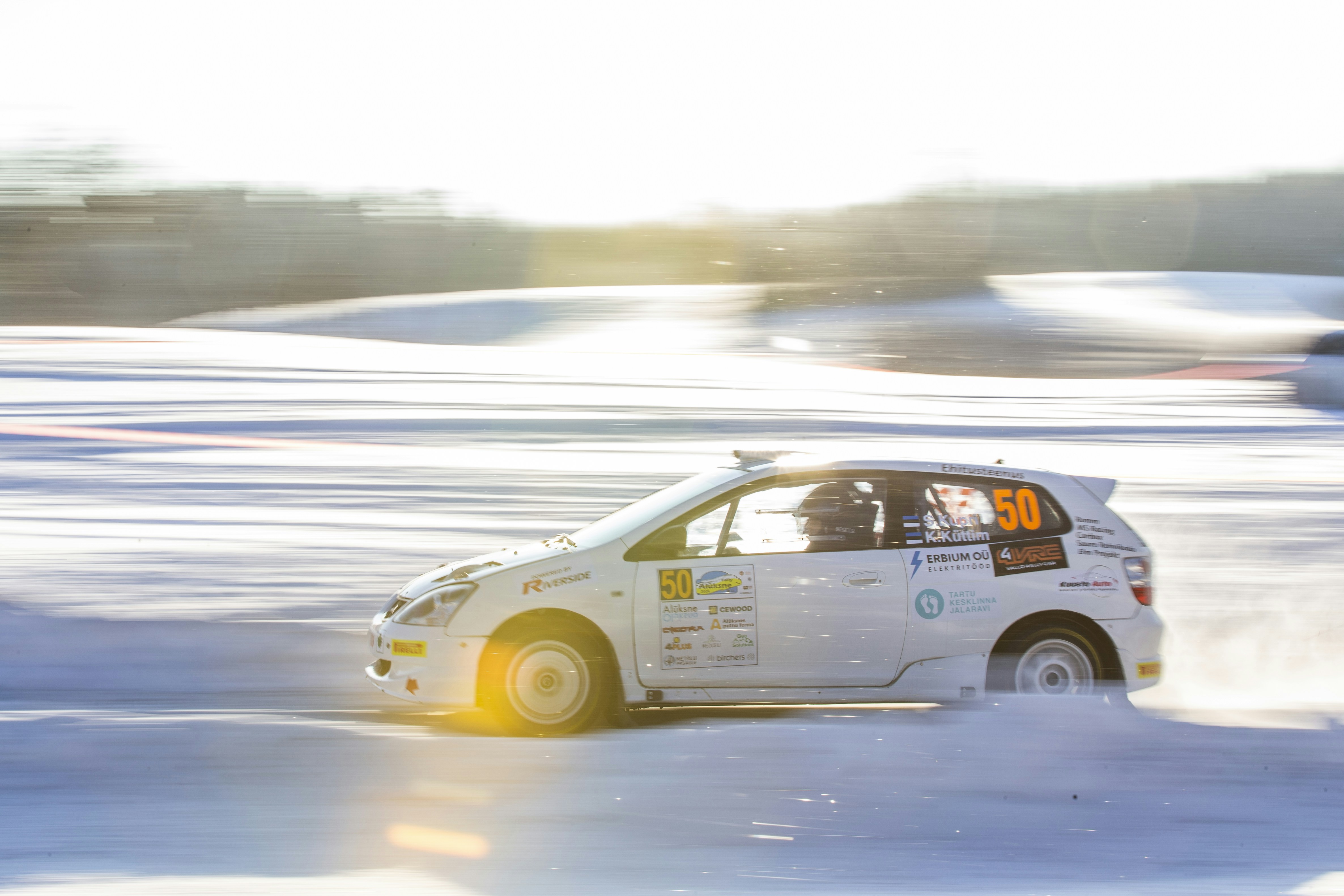 A white rally car races on a snowy track.