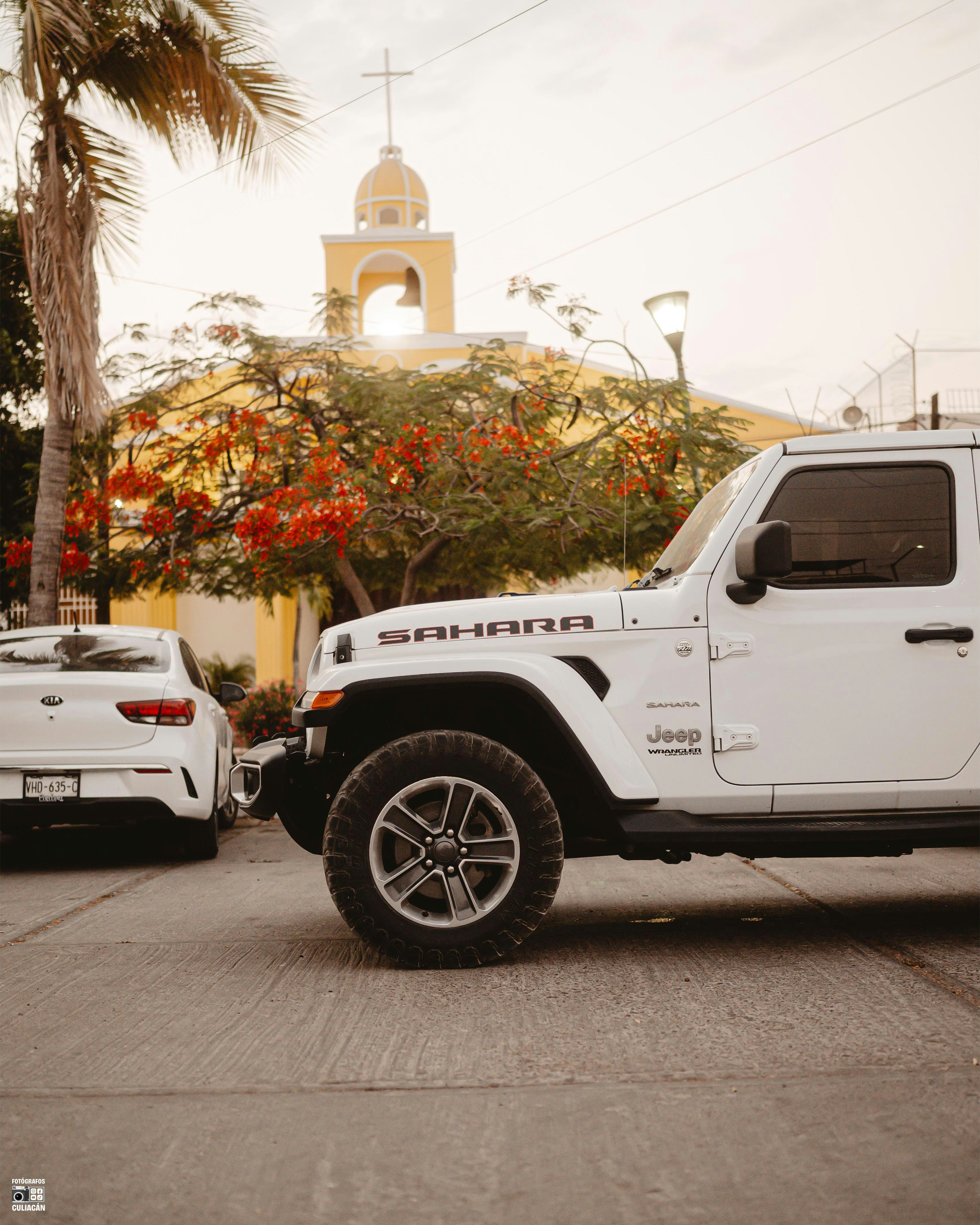 White Jeep Sahara Dominates a Sunlit Street with a Church Streaking in the Background