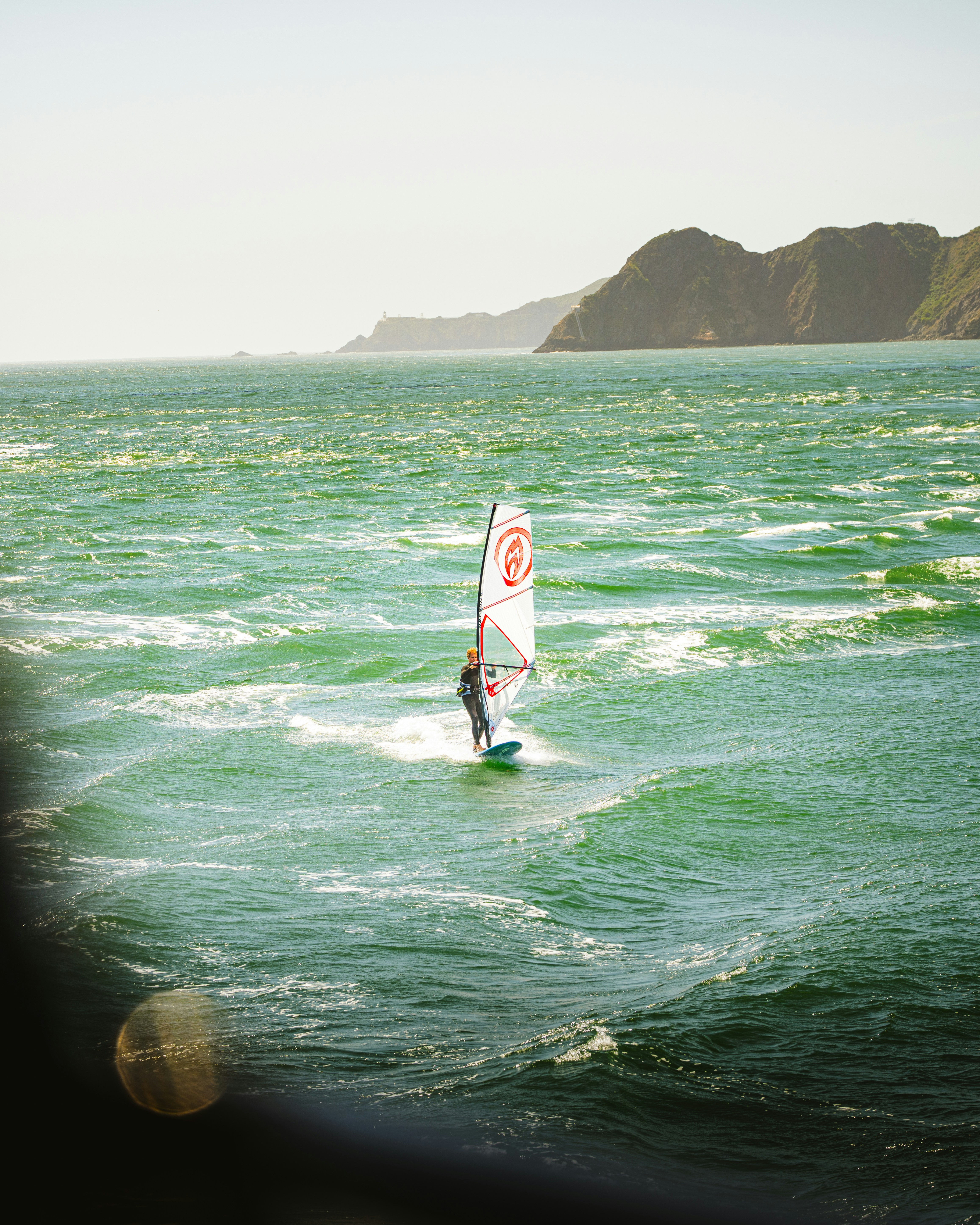 Windward Pulse: Windsurfer carving turquoise surf under sunlit cliffs
