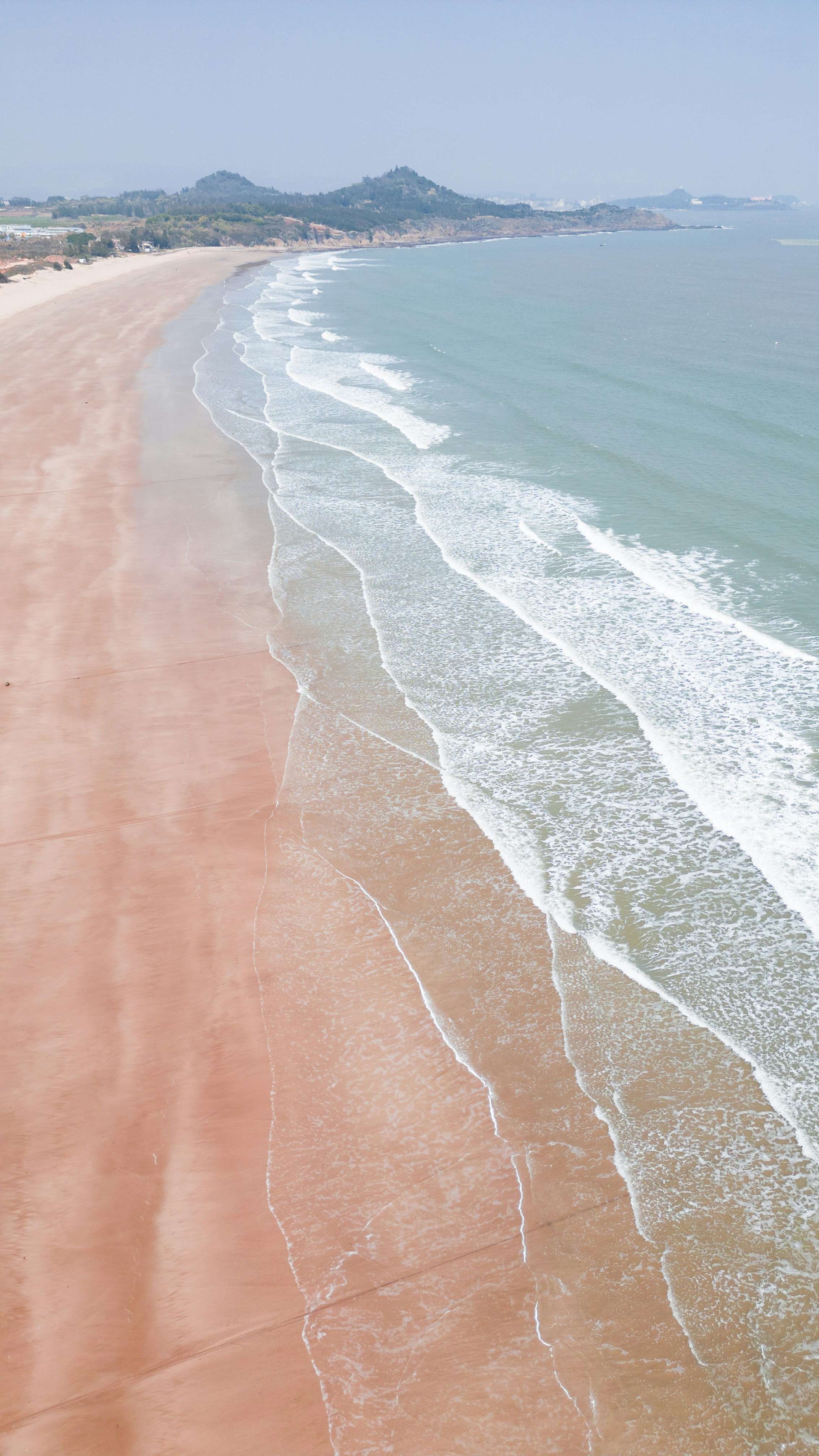 Long Coastal Veil: Aerial View of Wind-Swept Pink Sand and Quiet Waves