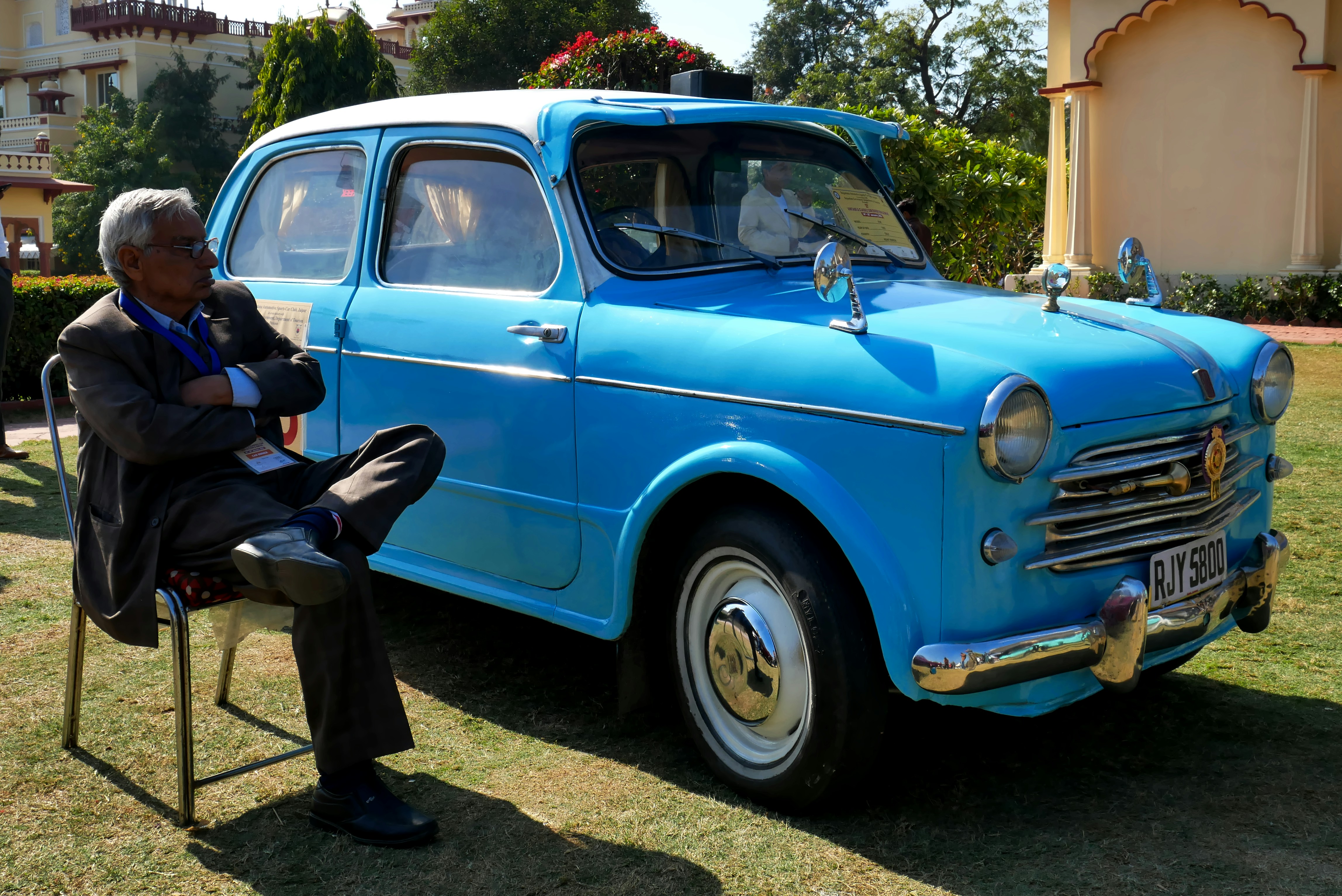 Blue vintage taxi under sun: a confiding elder seated beside the curb