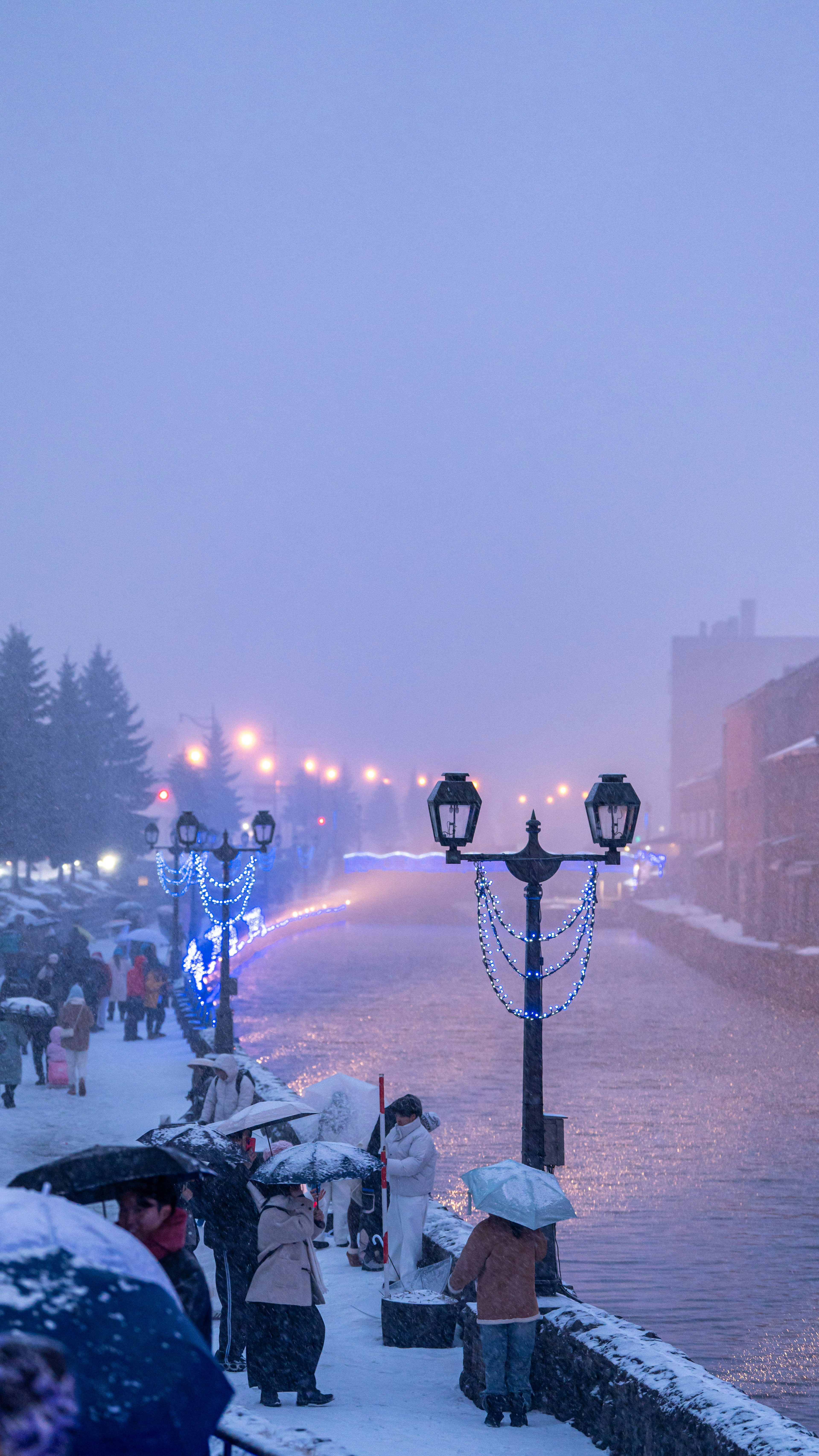 Snow-lit riverfront under winter dusk with festive icicle lights