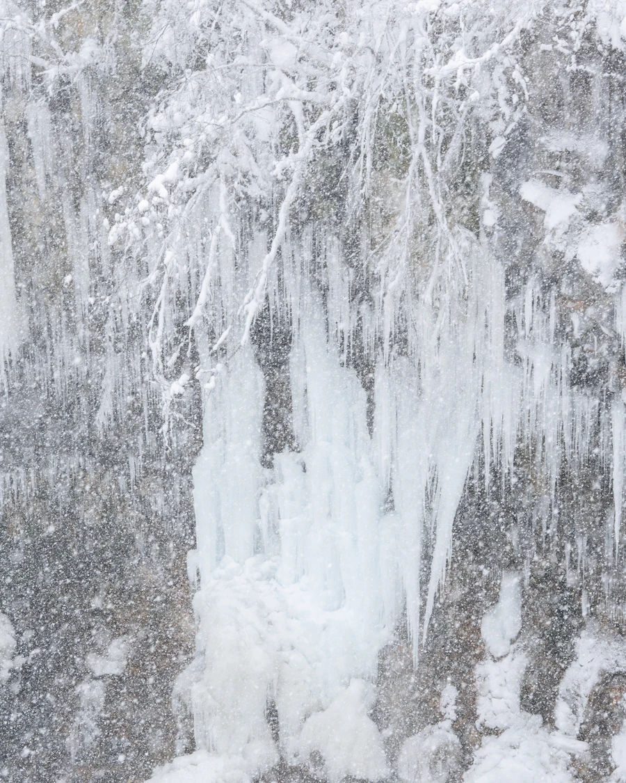 Close-up of a frozen window with elongated icicles and frost patterns creating a textured, monochrome winter scene. A glassy, abstract capture of ice formations.