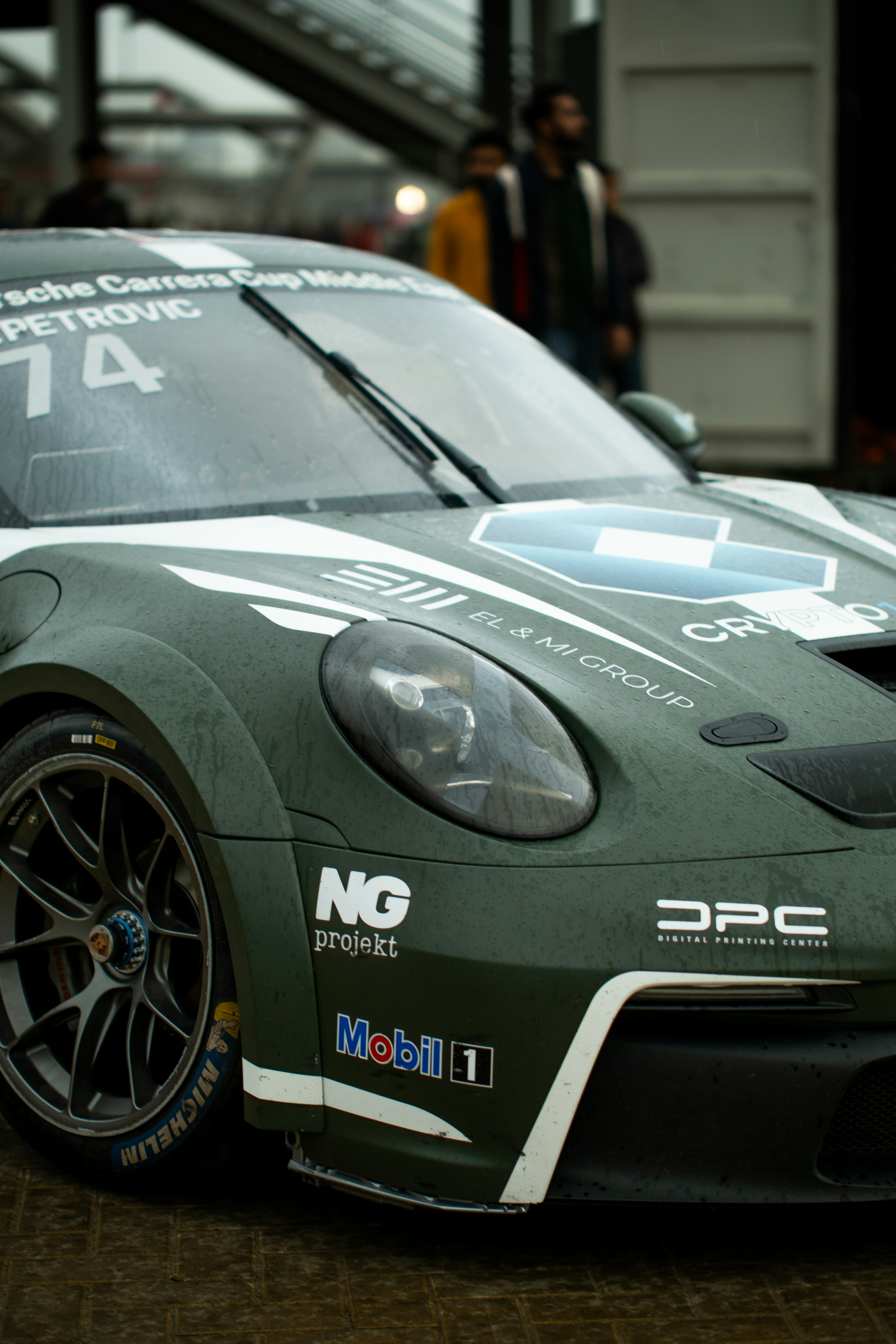 Green Porsche in Rain-Slicked Paddock: Close-Up of Racing Livery and Headlight Geometry