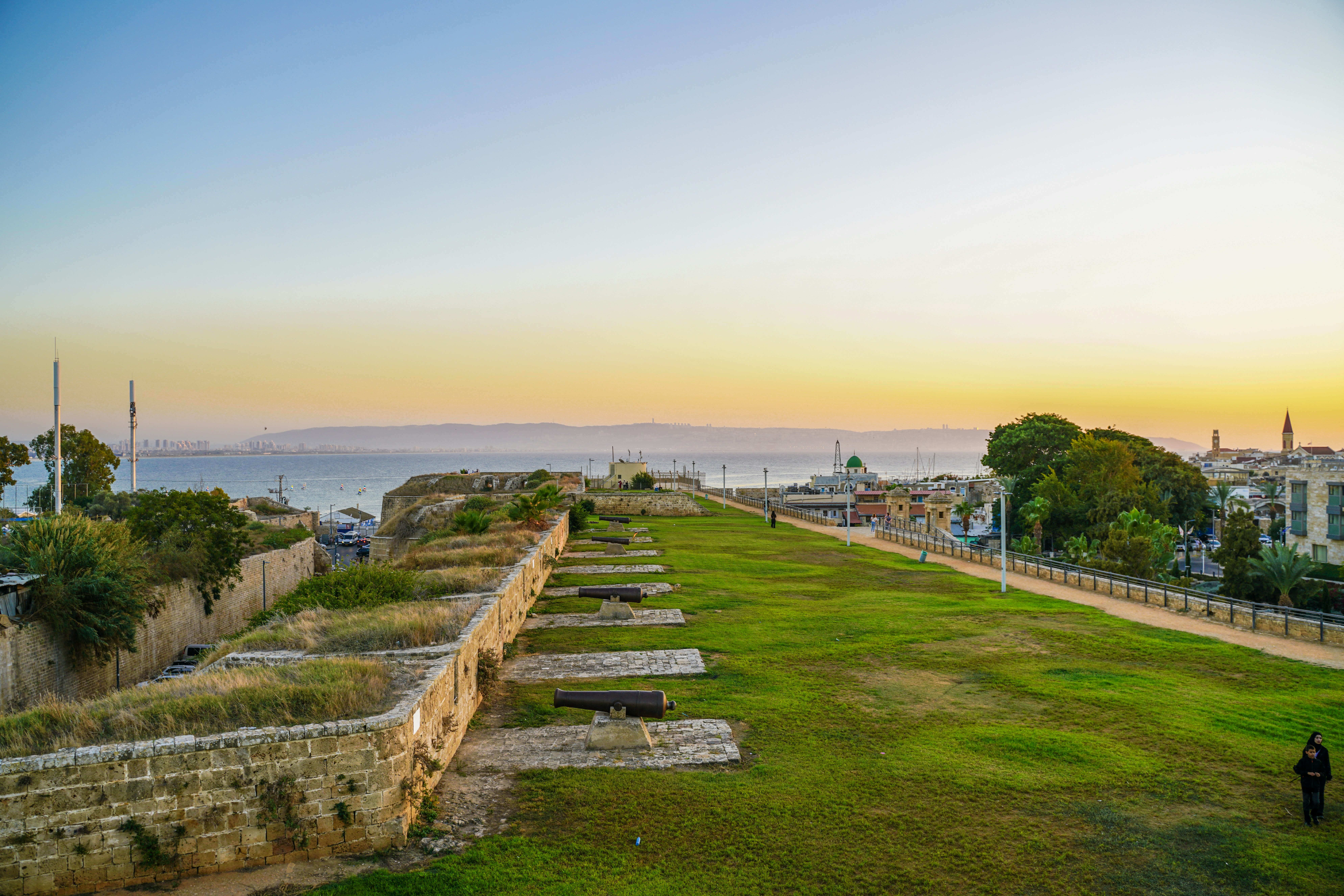 Sunset Over Fortified Promenade: Ruins, Green Verge, and Sea