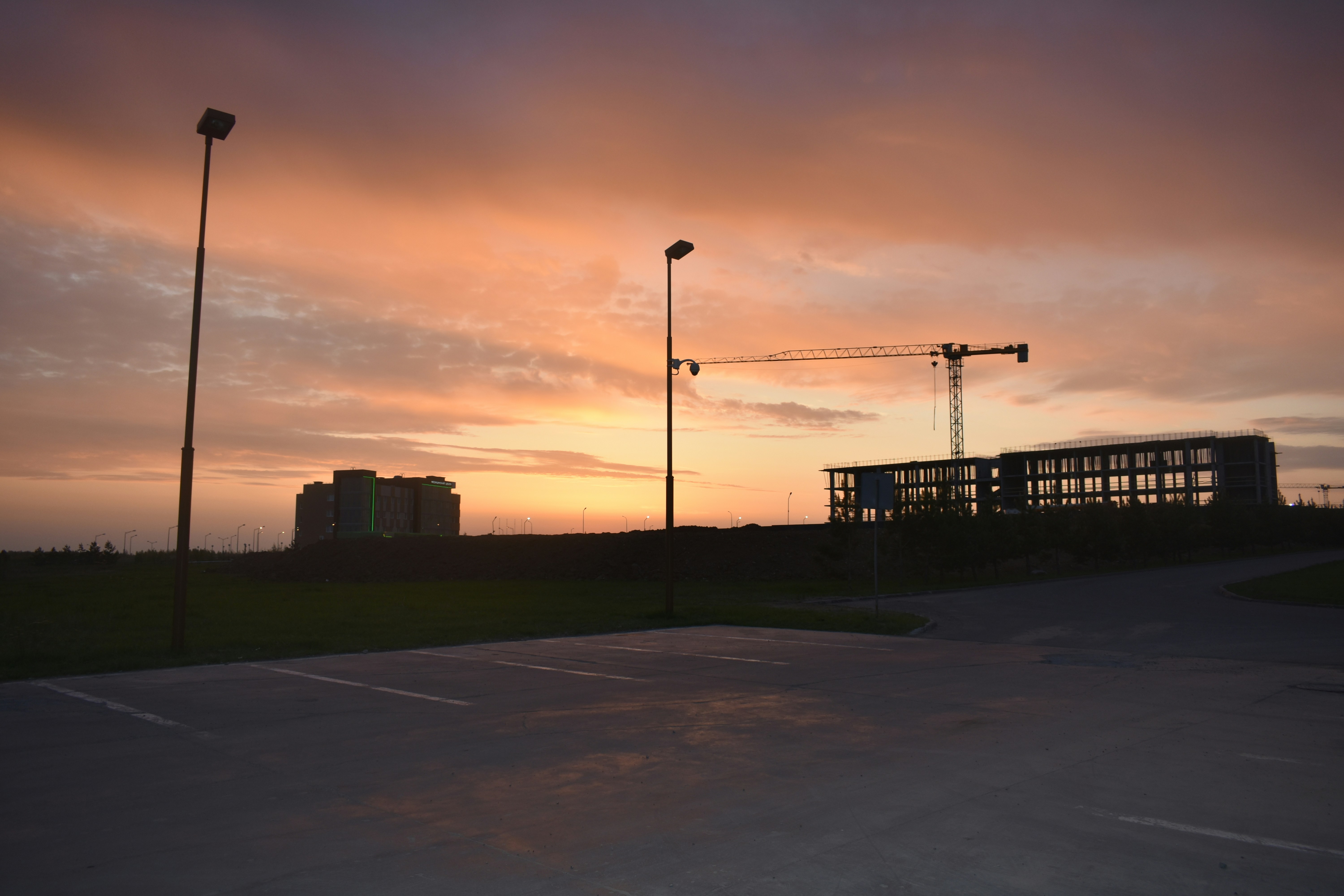 Dusk at the Construction Site: Lamps and Crane Silhouettes Over an Empty Parking Lot