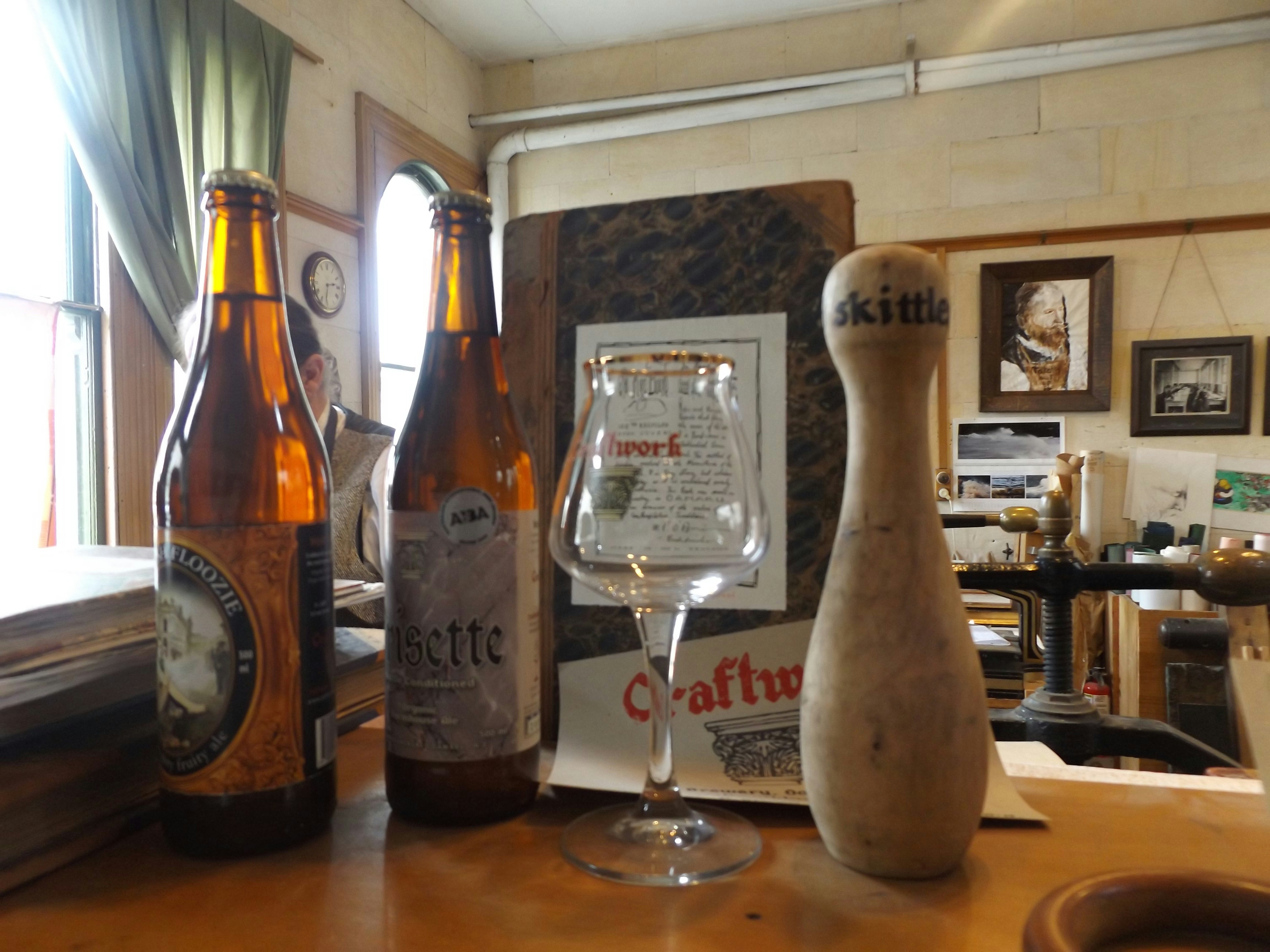 Two beer bottles, glass, and bowling pin on counter.