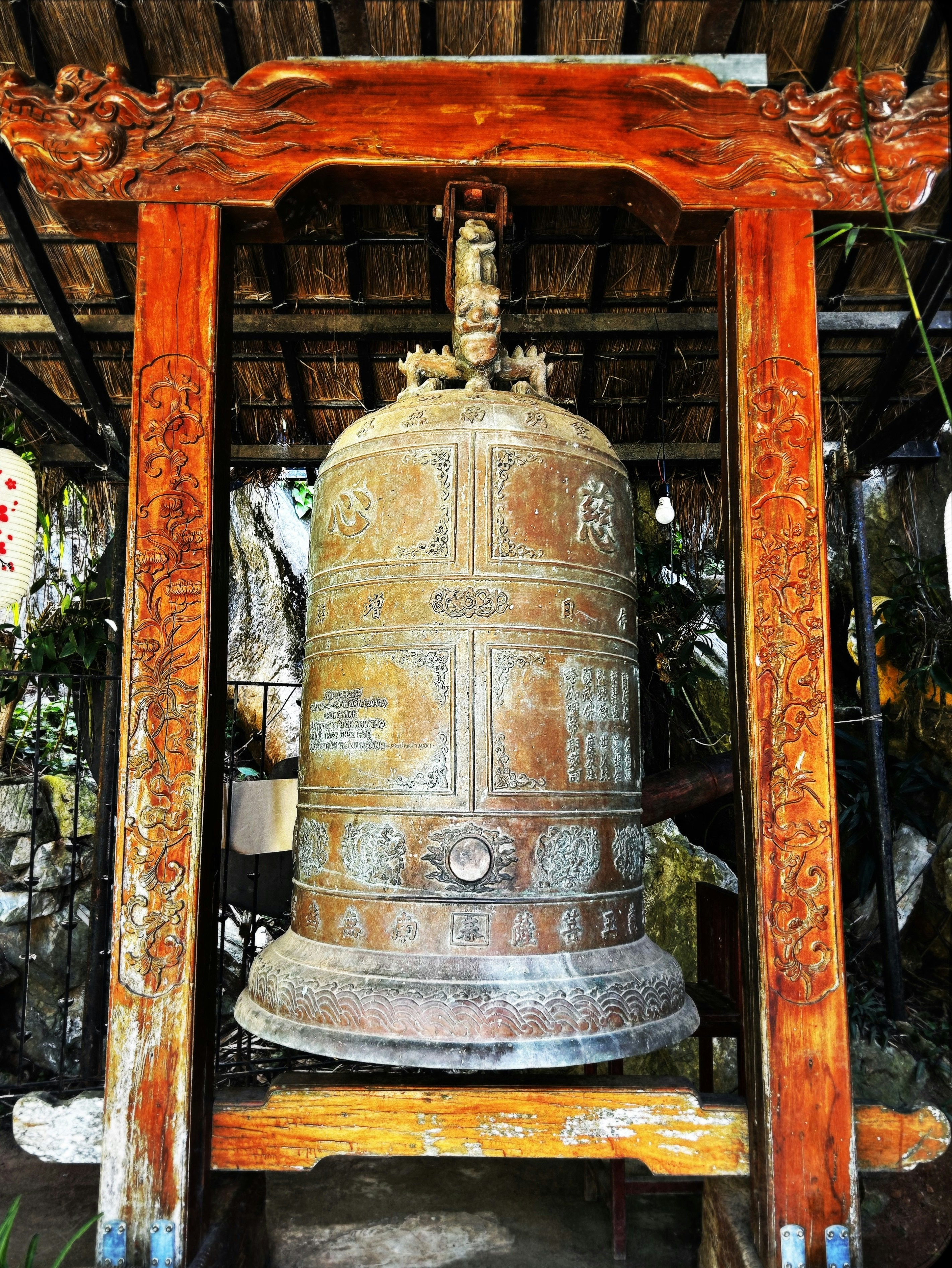 A Weathered Bell Framed by Ornate Carved Frame in a Sacred Courtyard