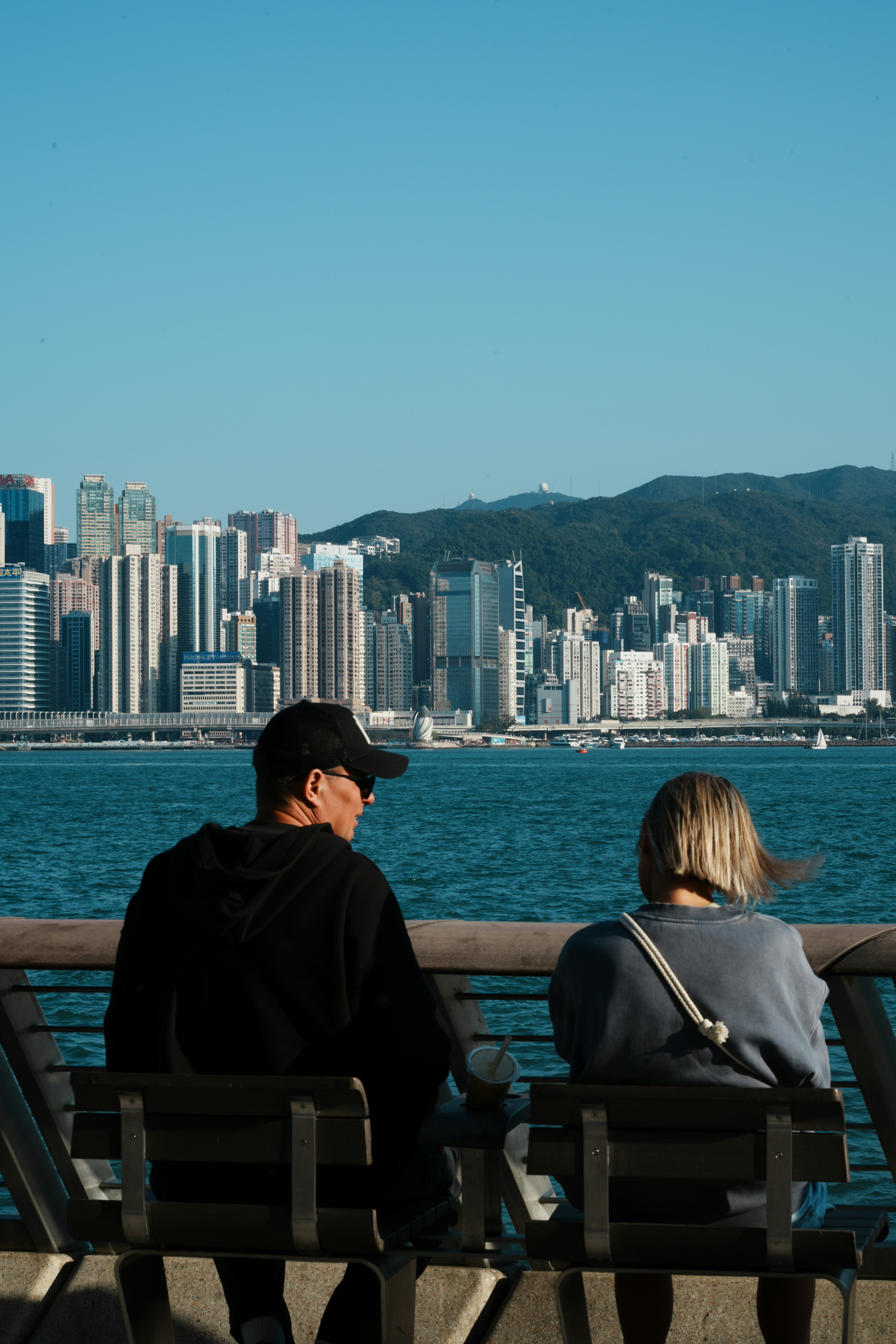 Cityview Serenade: Two on a Sea-Facing Bench Amid Skyscraper Horizon