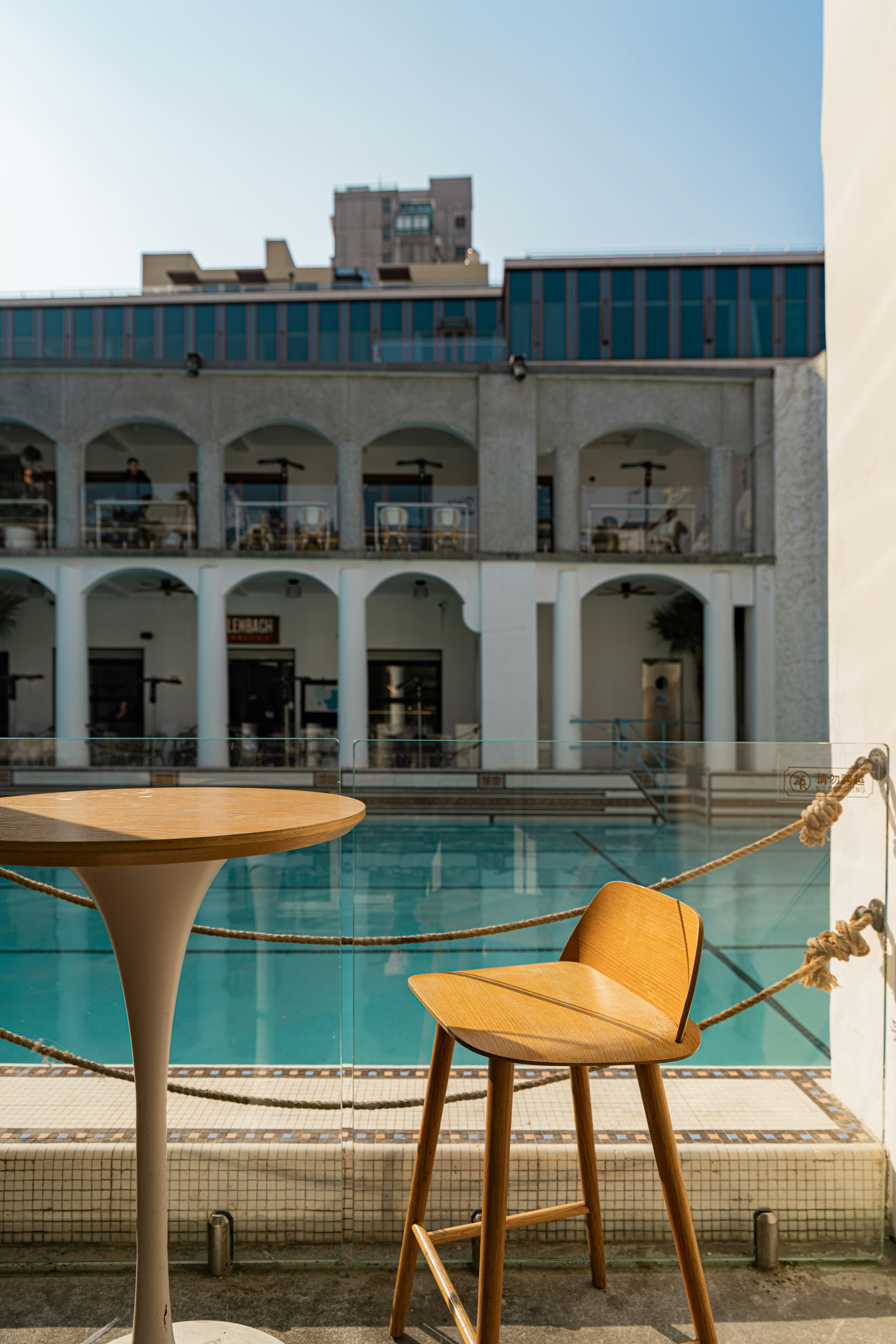 Rooftop Terrace: A Citrus Wood Stool, Sunlit Table, and Glassy Poolscape