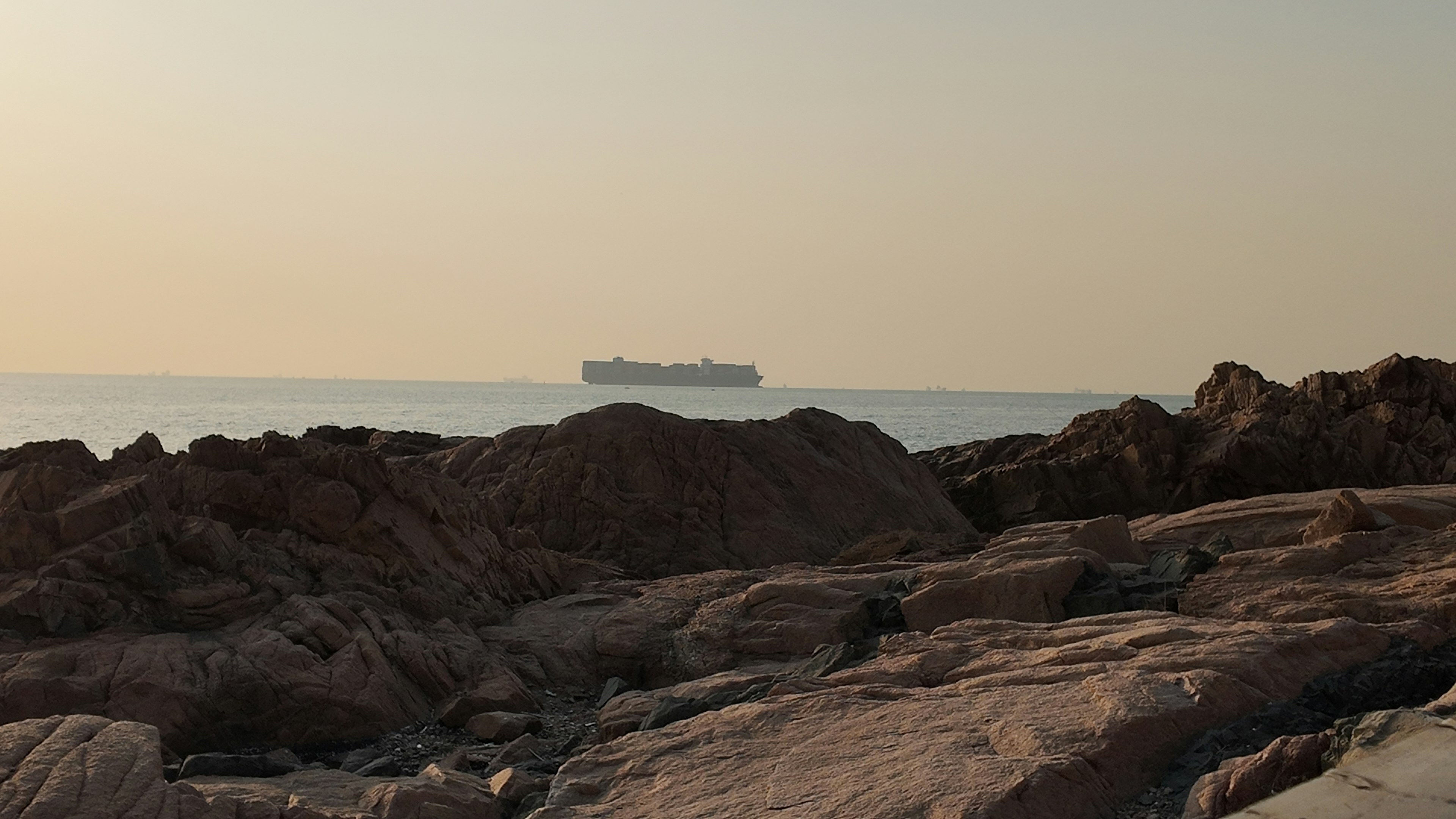 A cargo ship sails on the ocean near rocky shore.
